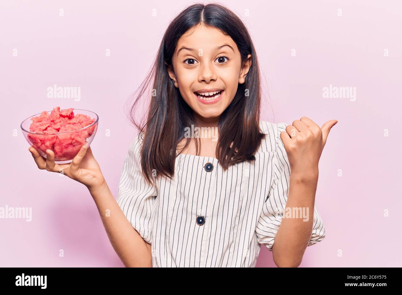 Beautiful child girl holding ice cream pointing thumb up to the side ...