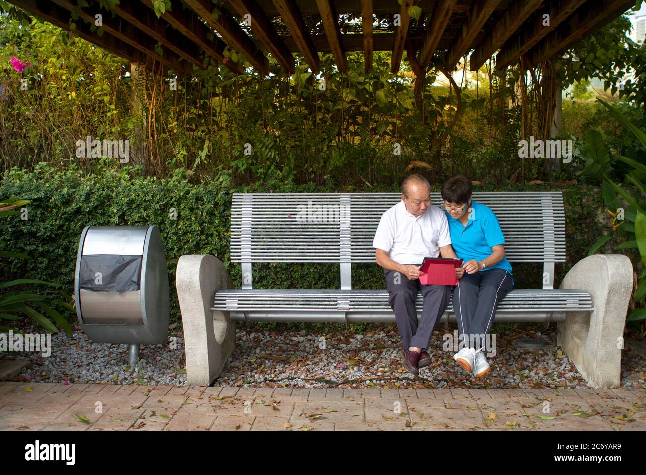 Elderly Chinese couple sitting on a bench and reading a mobile tablet ...