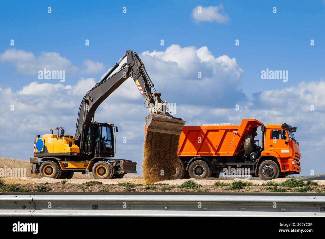 A yellow backhoe loader loads the earth into a truck during the ...