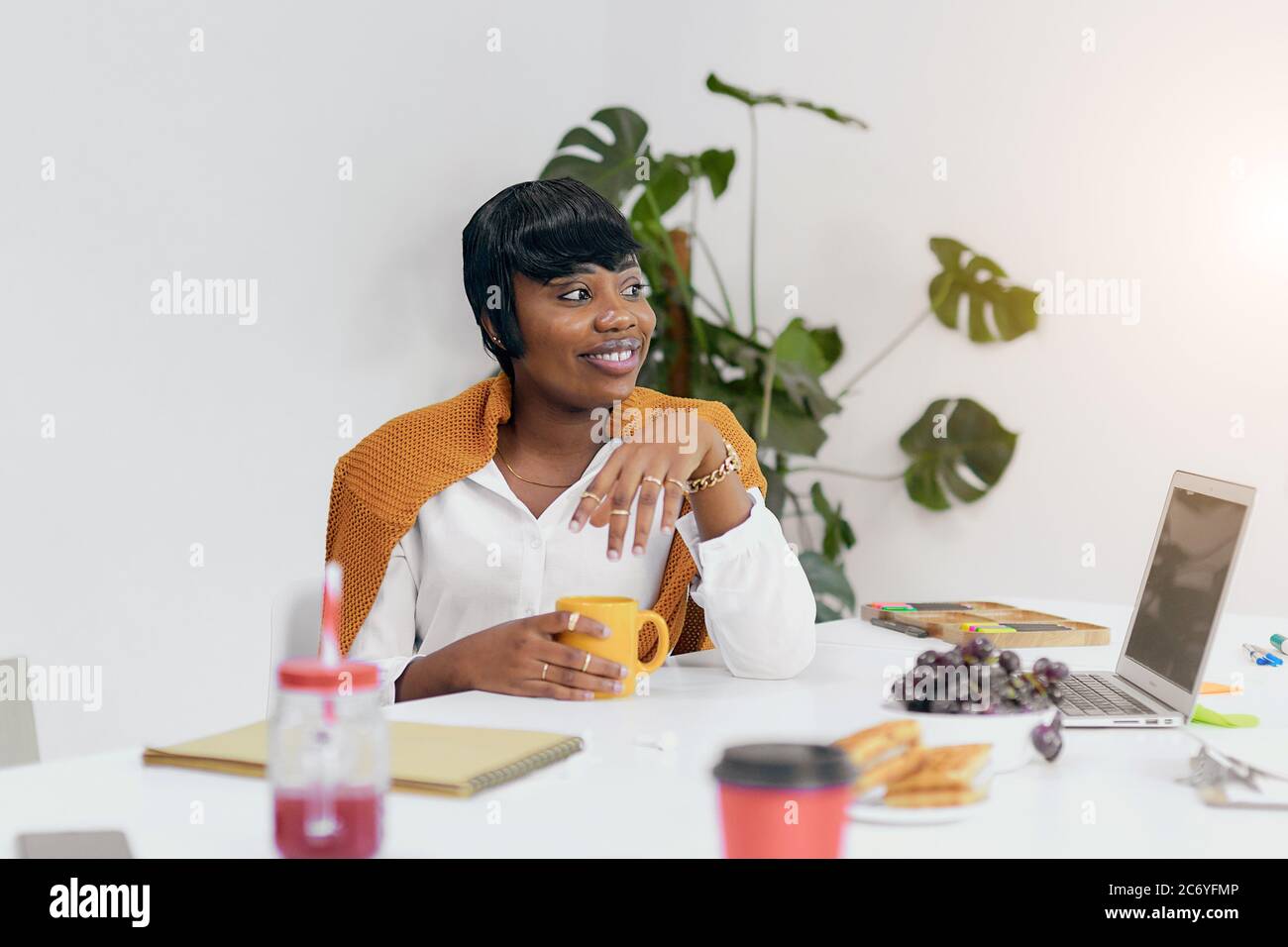 Attractive african lady sitting in office with cup of coffee or tea ...
