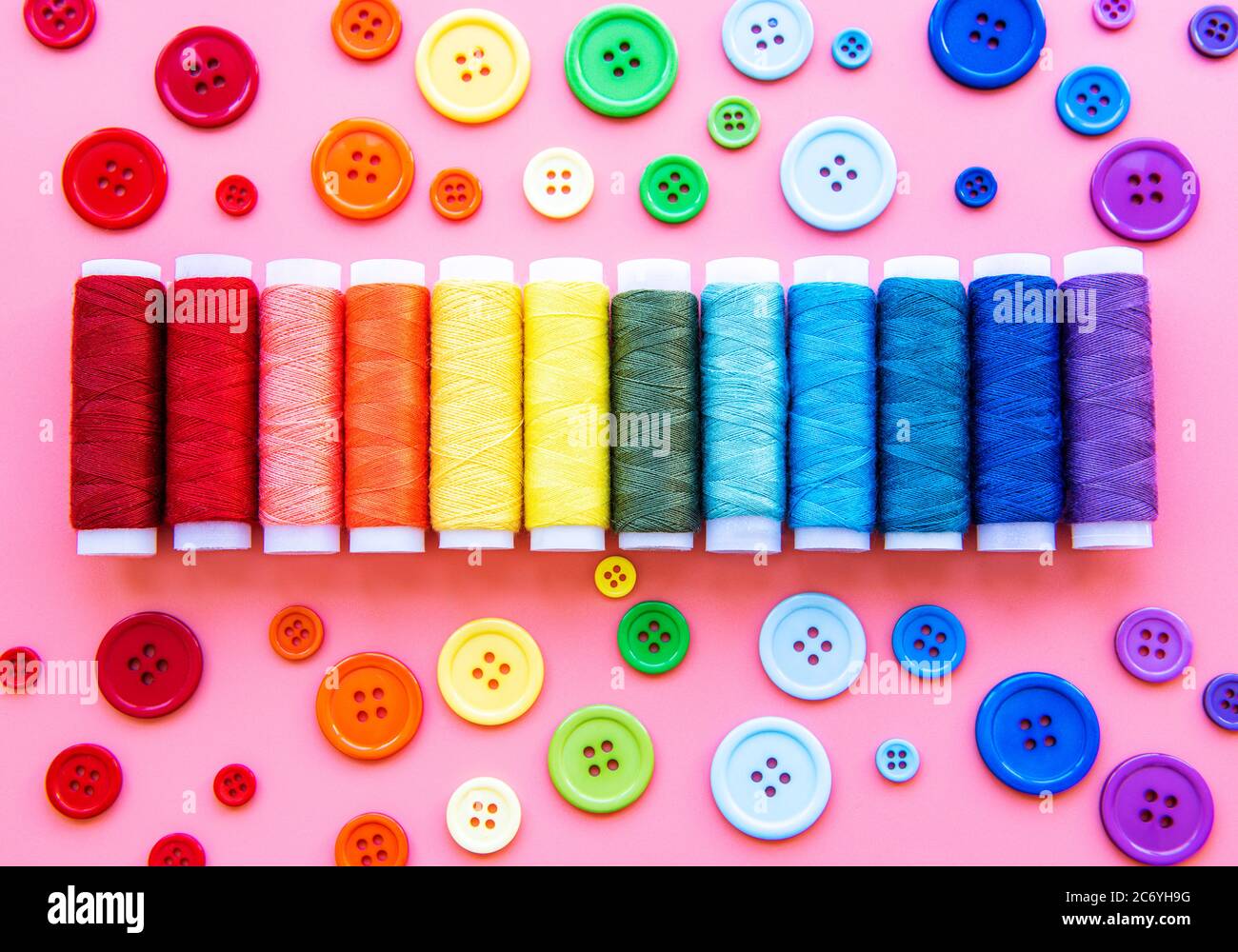 Spools of thread and buttons on the colors of the rainbow on a pink ...