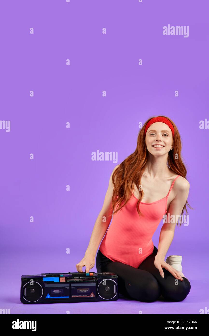 athletic red-haired female trainer sits near portable retro audio ...