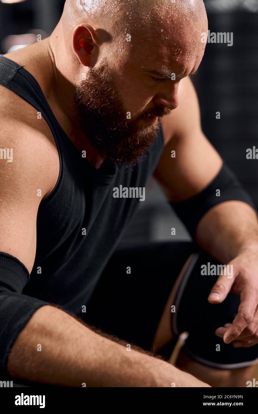 Close up of brutal beard tired bodybuilder sitting on floor, looking ...