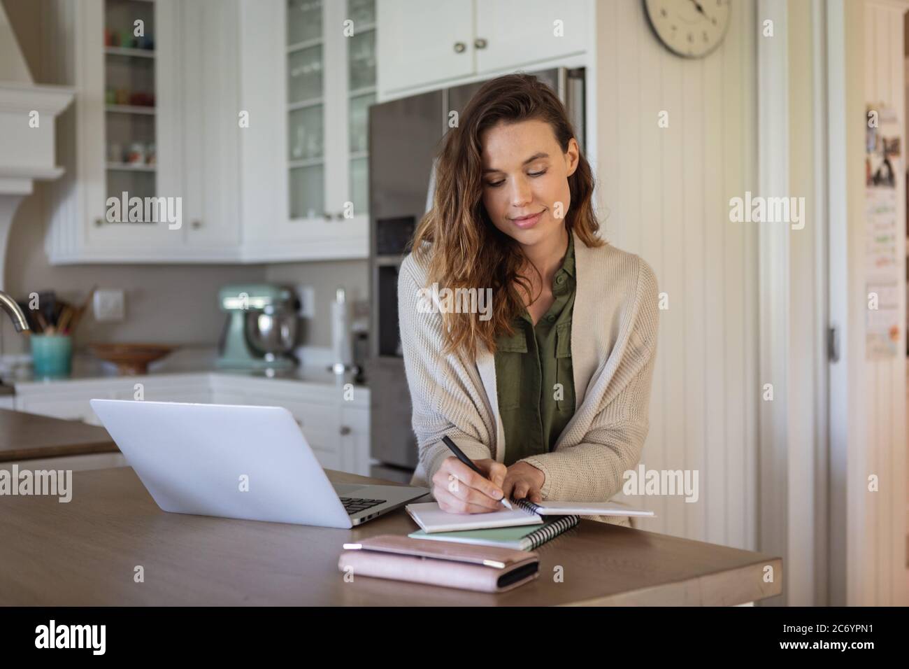 Woman taking notes while using laptop in the kitchen Stock Photo - Alamy