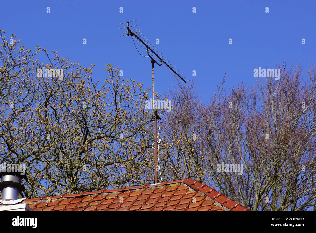 Old television antenna on a roof with roof tiles and with a blue sky ...