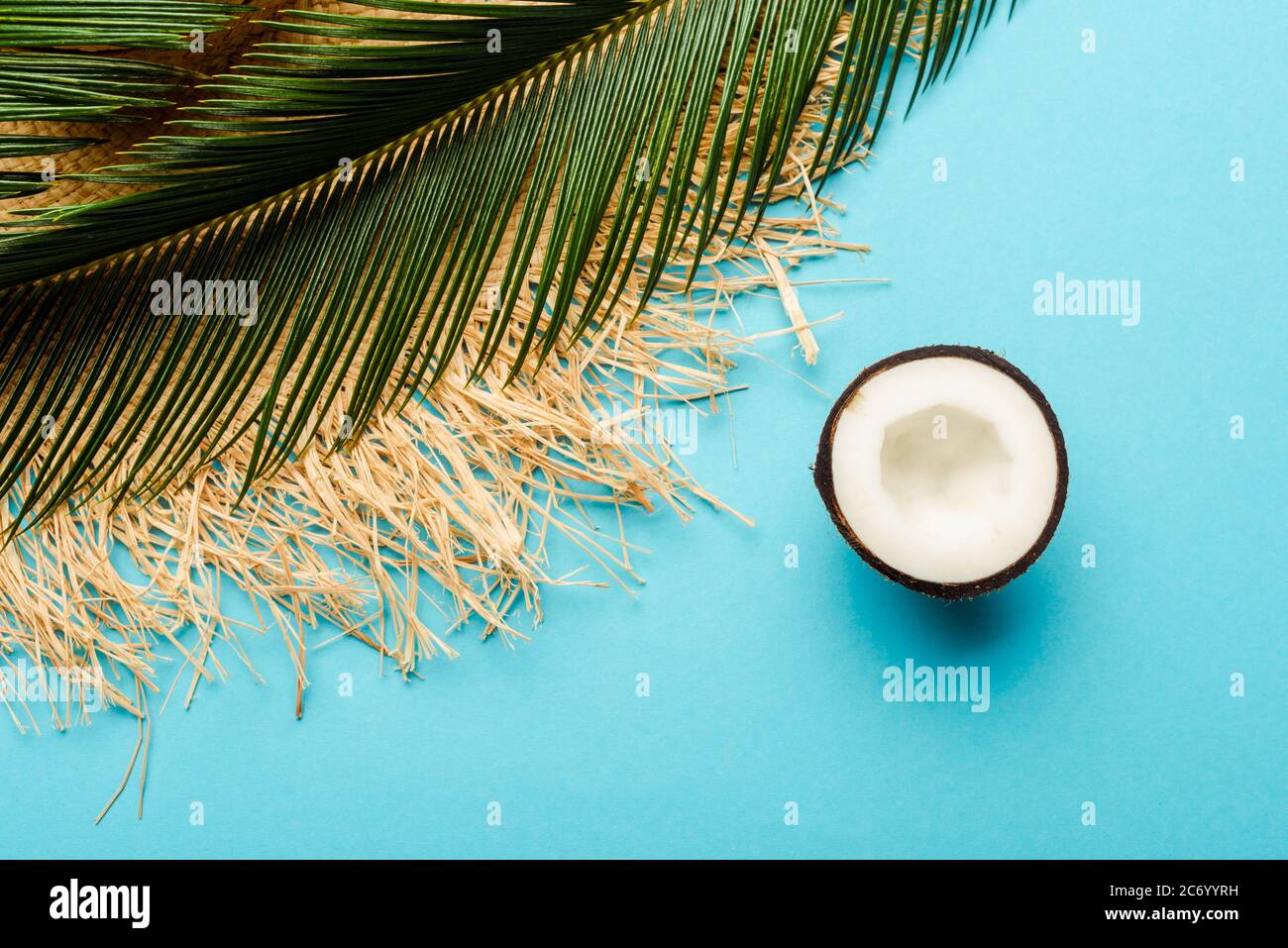 top view of green palm leaf, coconut half, straw hat on blue background ...