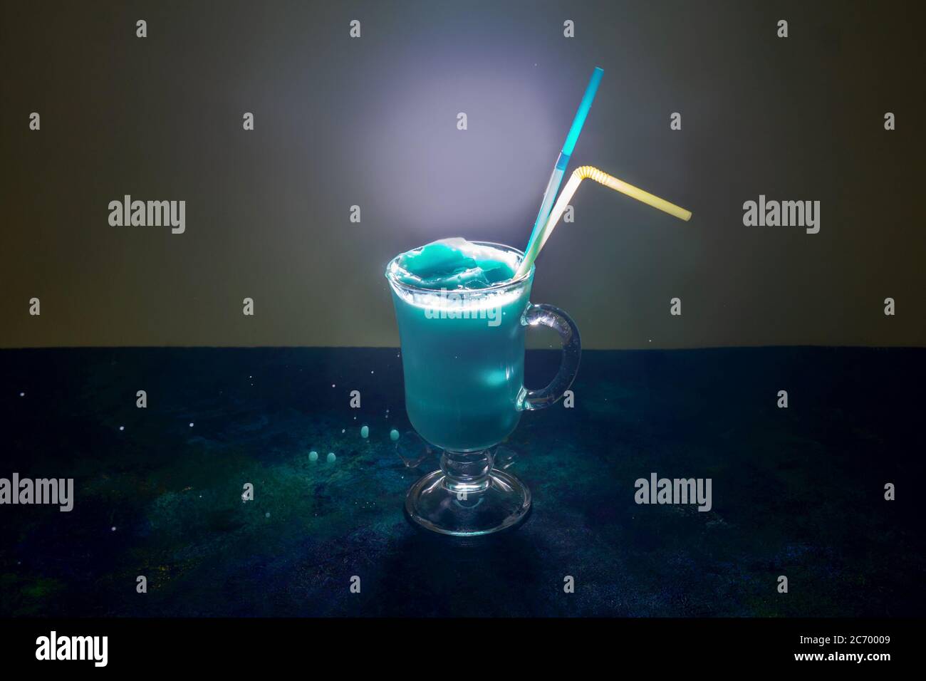 Blue cocktail in glass with splash on the dark background. Two tubes ...