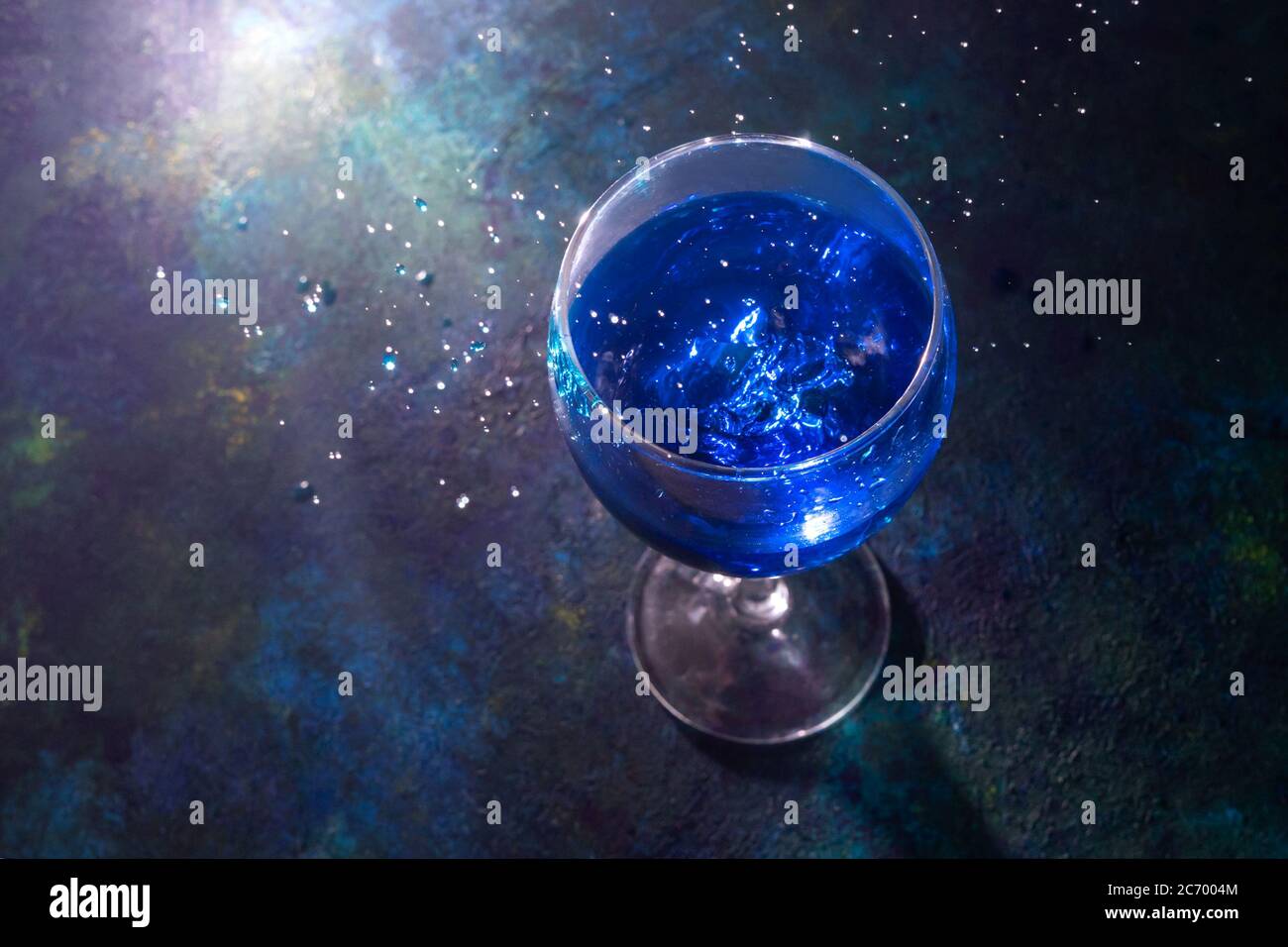 Blue cocktail in wineglass with splash on dark background with back ...