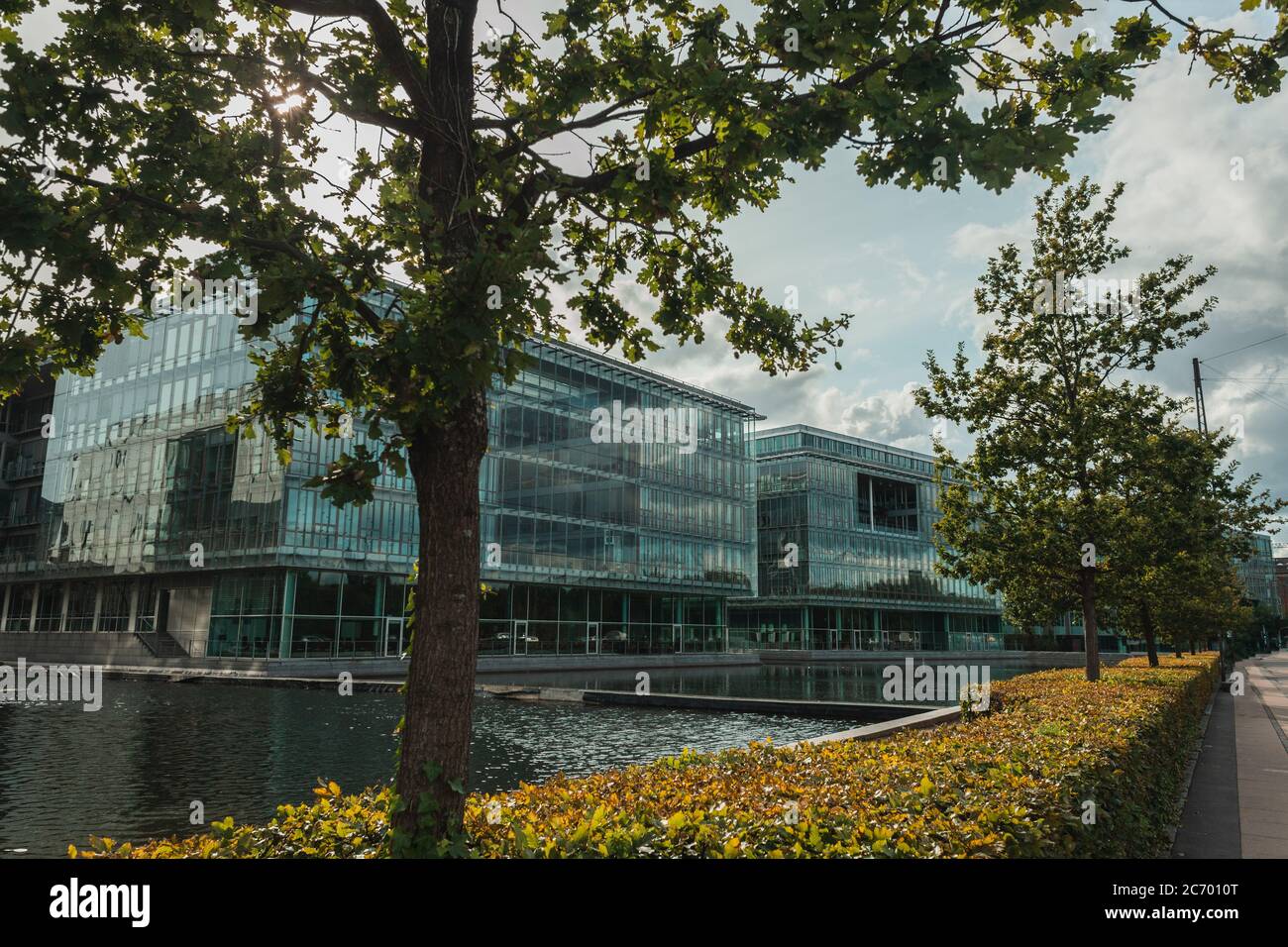 Trees near canal and building with glass facade on urban street ...