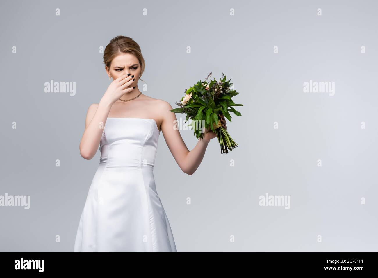 bride in white wedding dress touching nose while holding smelly flowers ...