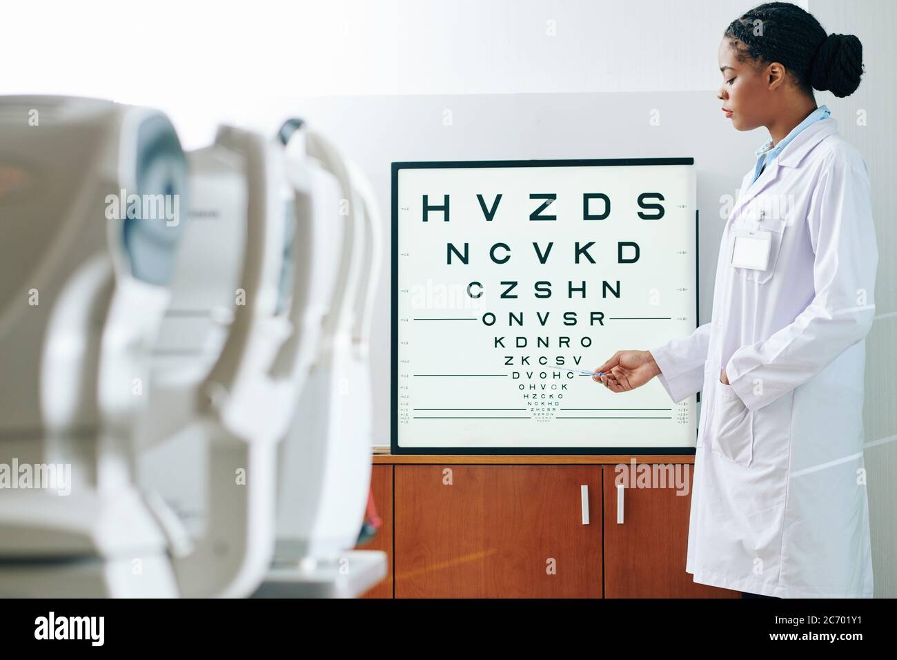 Serious young Black ophthalmologist pointing at letters on testing ...