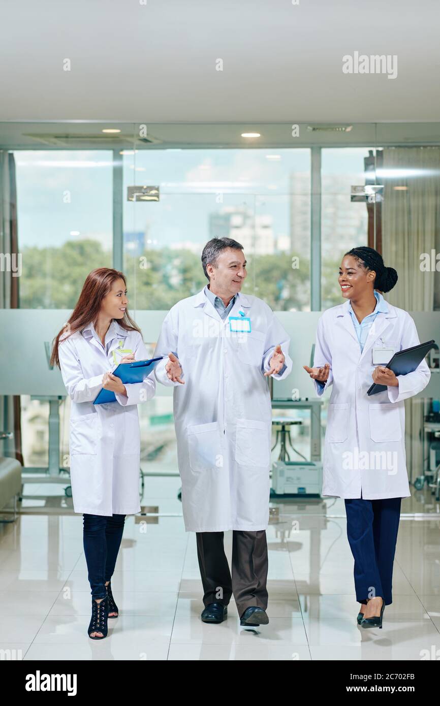 Happy mature doctor walking through clinic corrridor and talking to ...