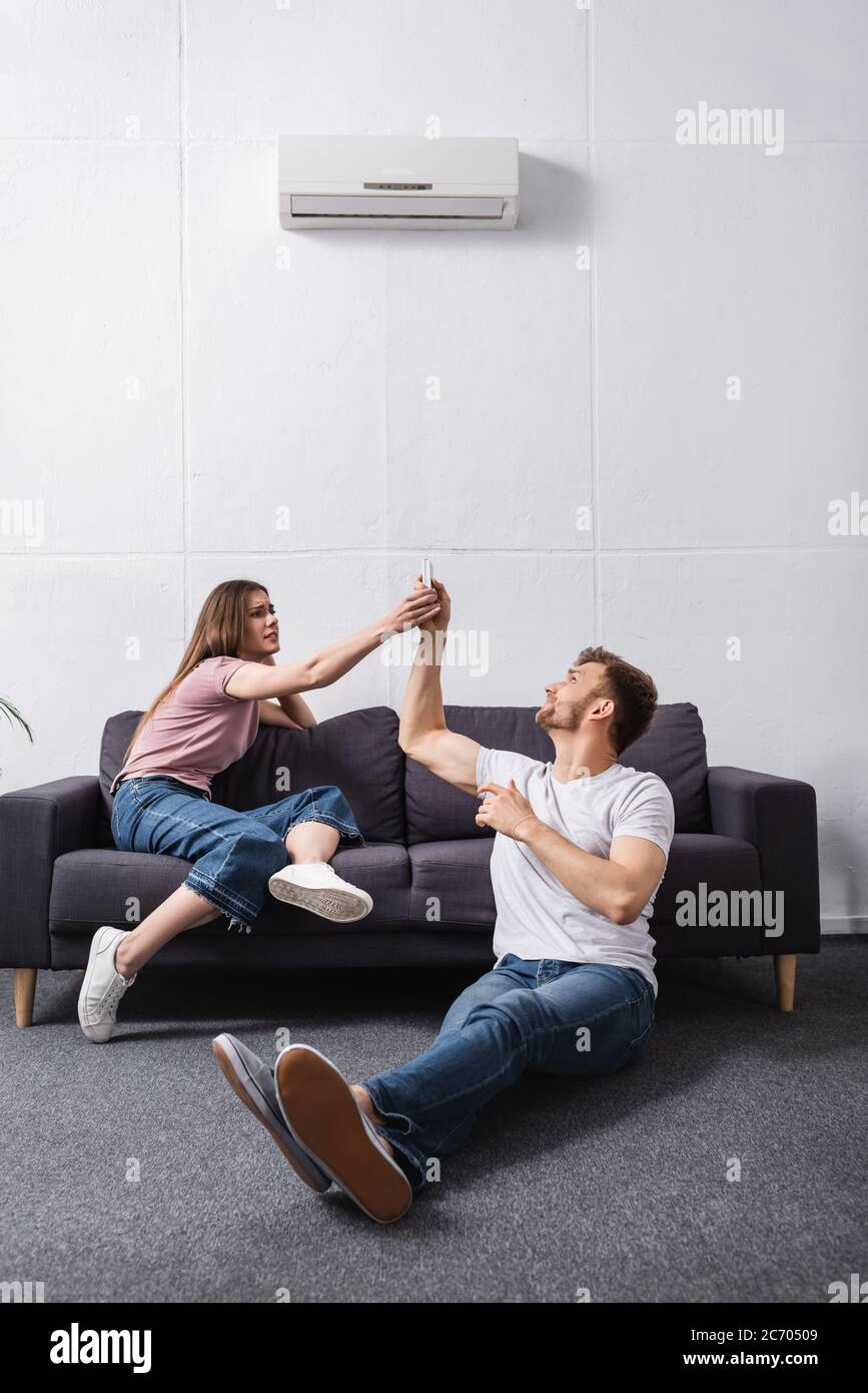 angry couple with remote controller at home with broken air conditioner ...