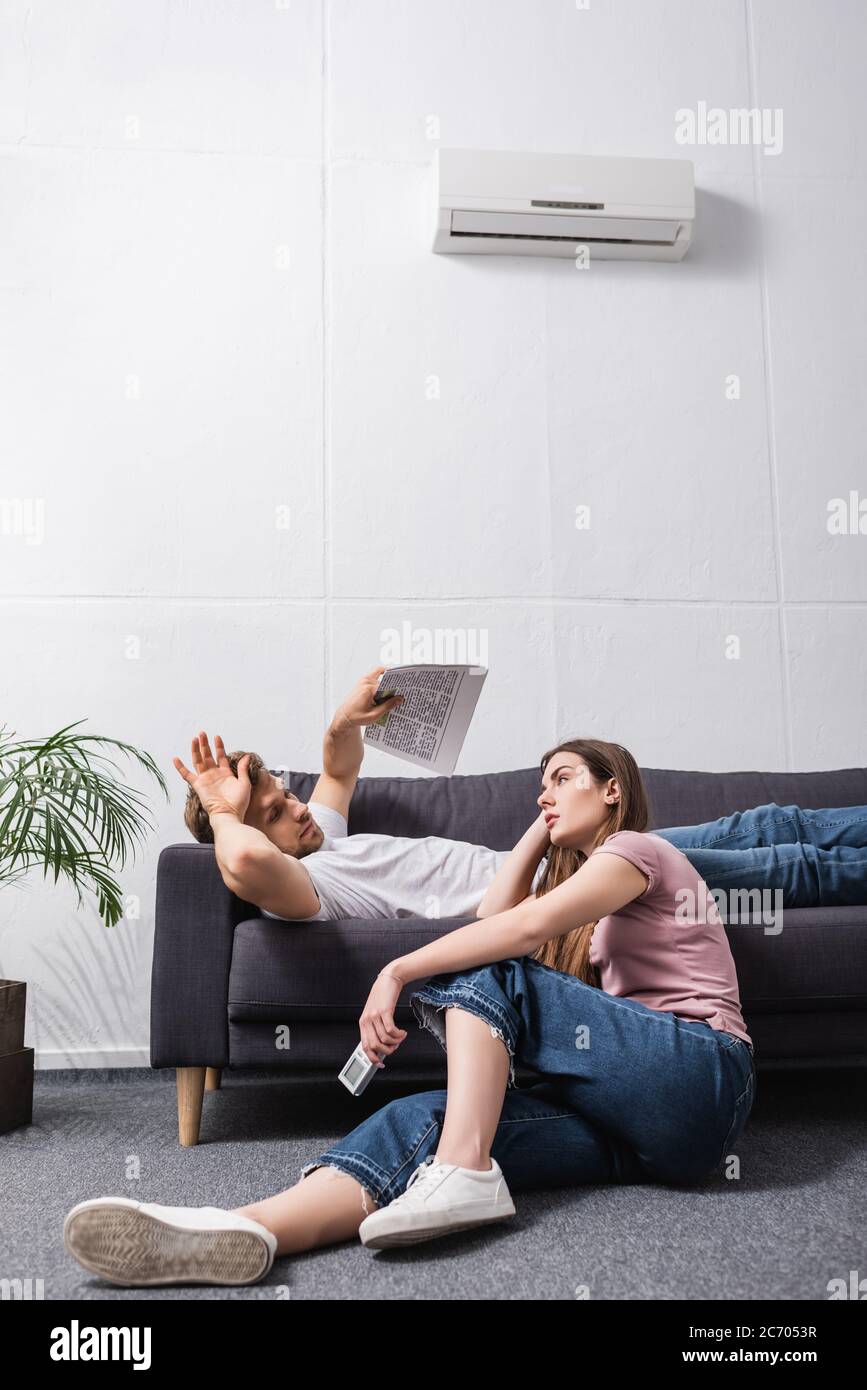 sad couple with remote controller suffering from heat at home with ...