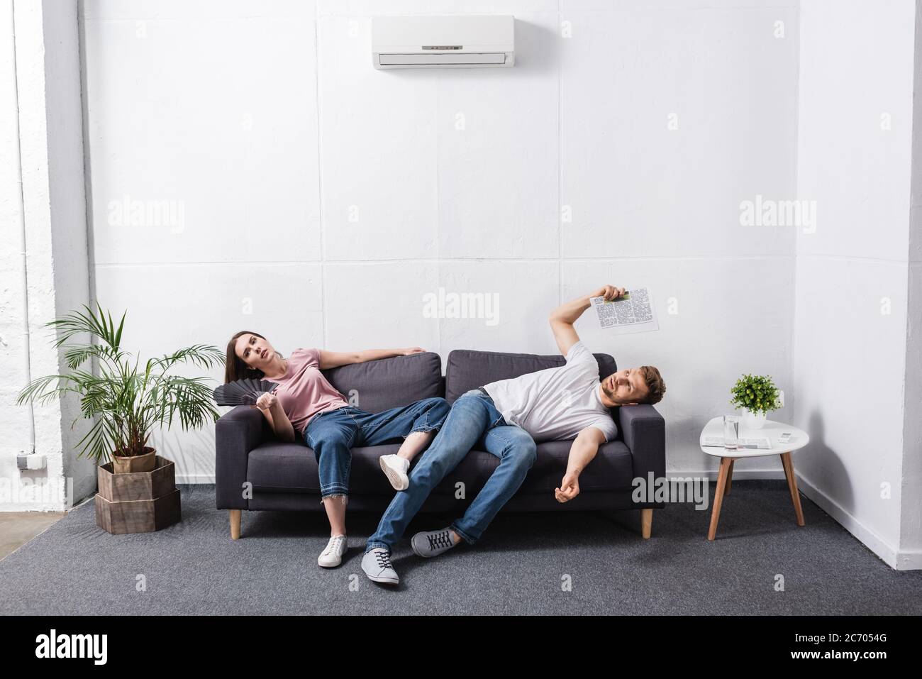 sad couple with hand fan and newspaper suffering from heat at home with ...