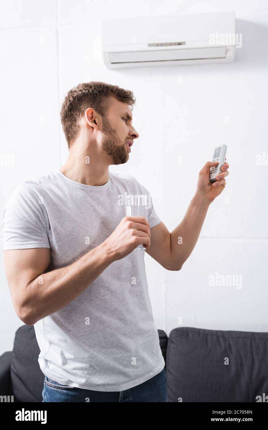 sad man holding glass of water while trying to switch on air ...