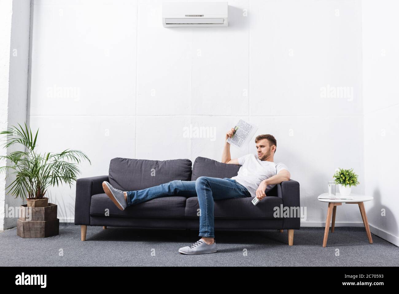 young man suffering from heat while using newspaper as hand fan at home ...