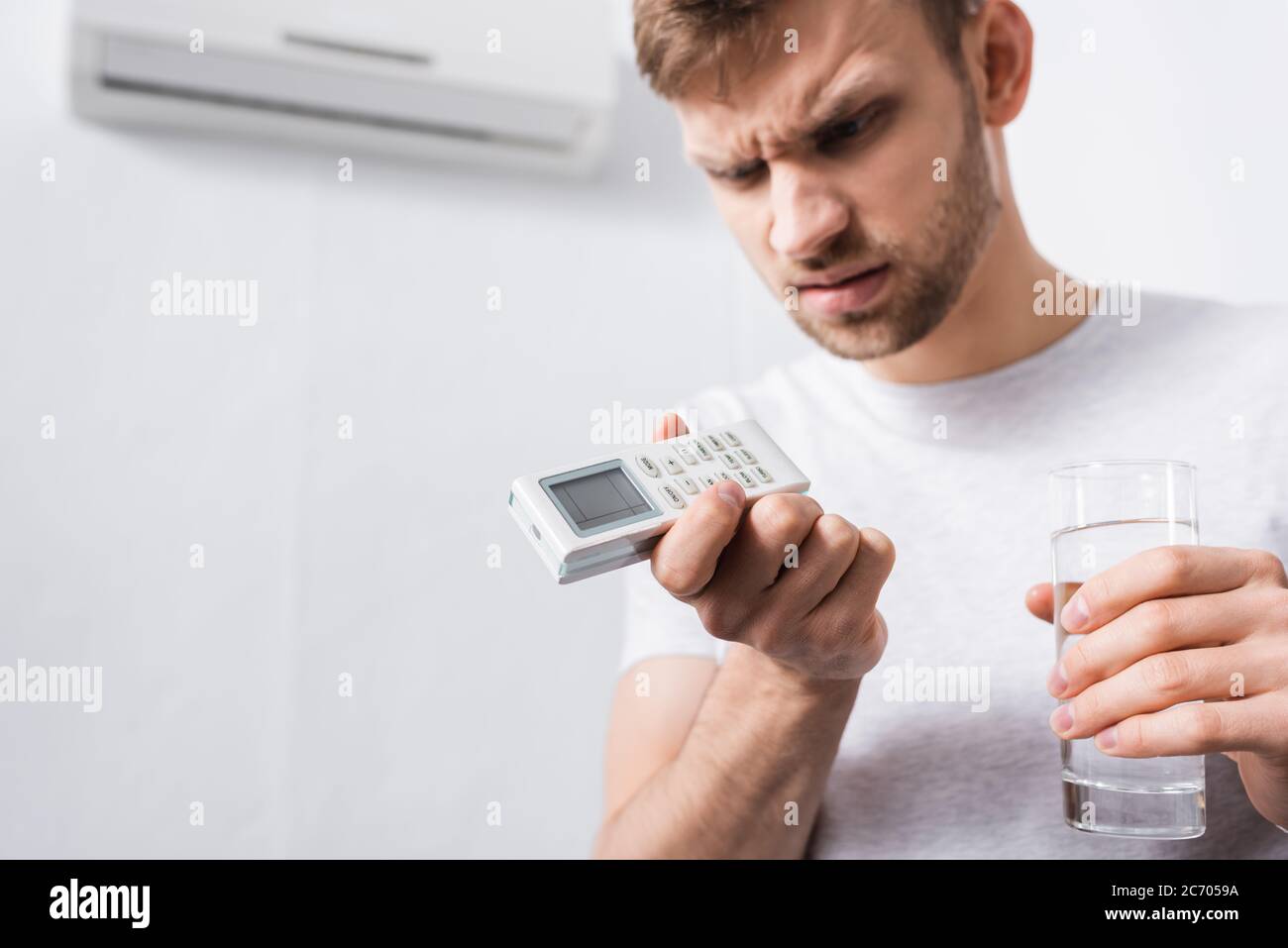 angry man holding glass of water while trying to switch on air ...