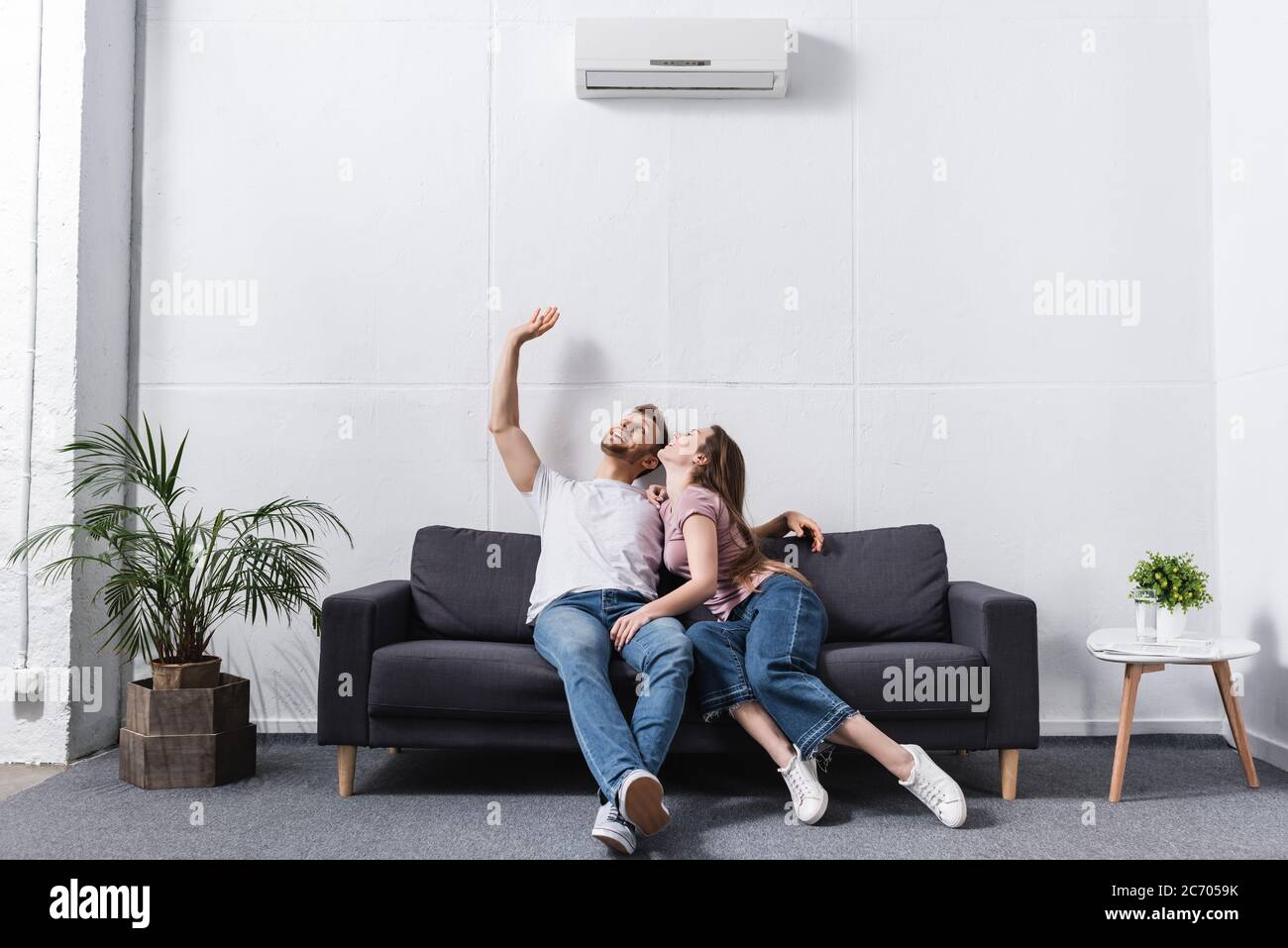 smiling girlfriend and boyfriend hugging at home with air conditioner ...