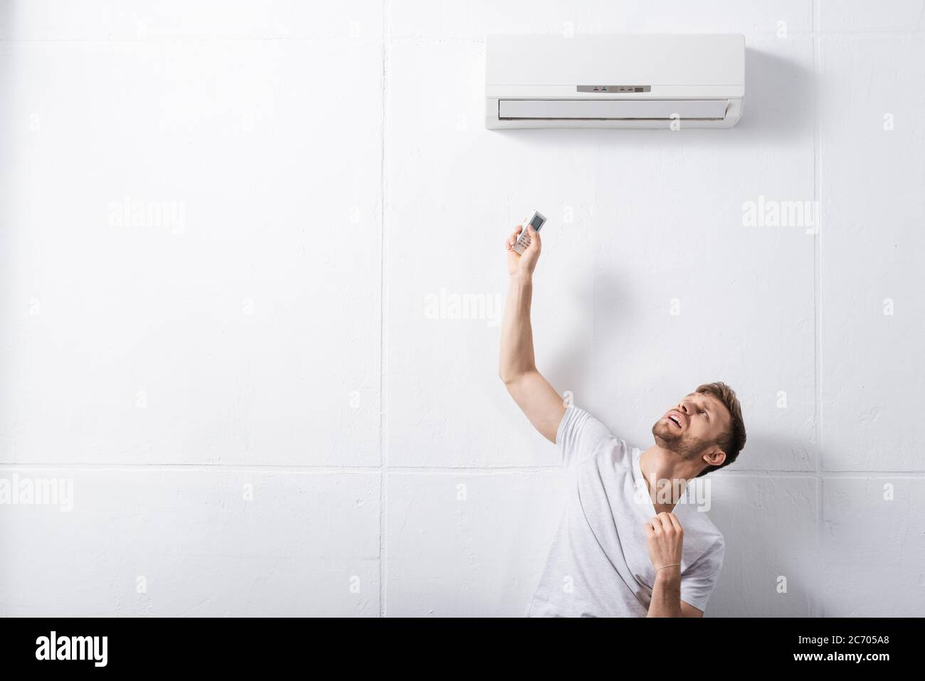 confused man holding remote controller and suffering from heat with ...