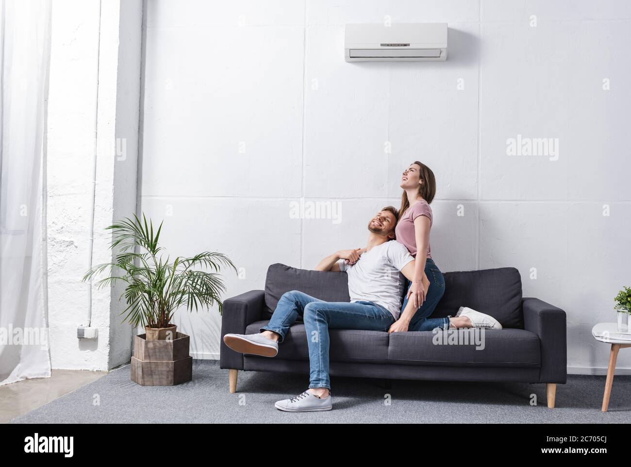 smiling girlfriend and boyfriend hugging at home with air conditioner ...