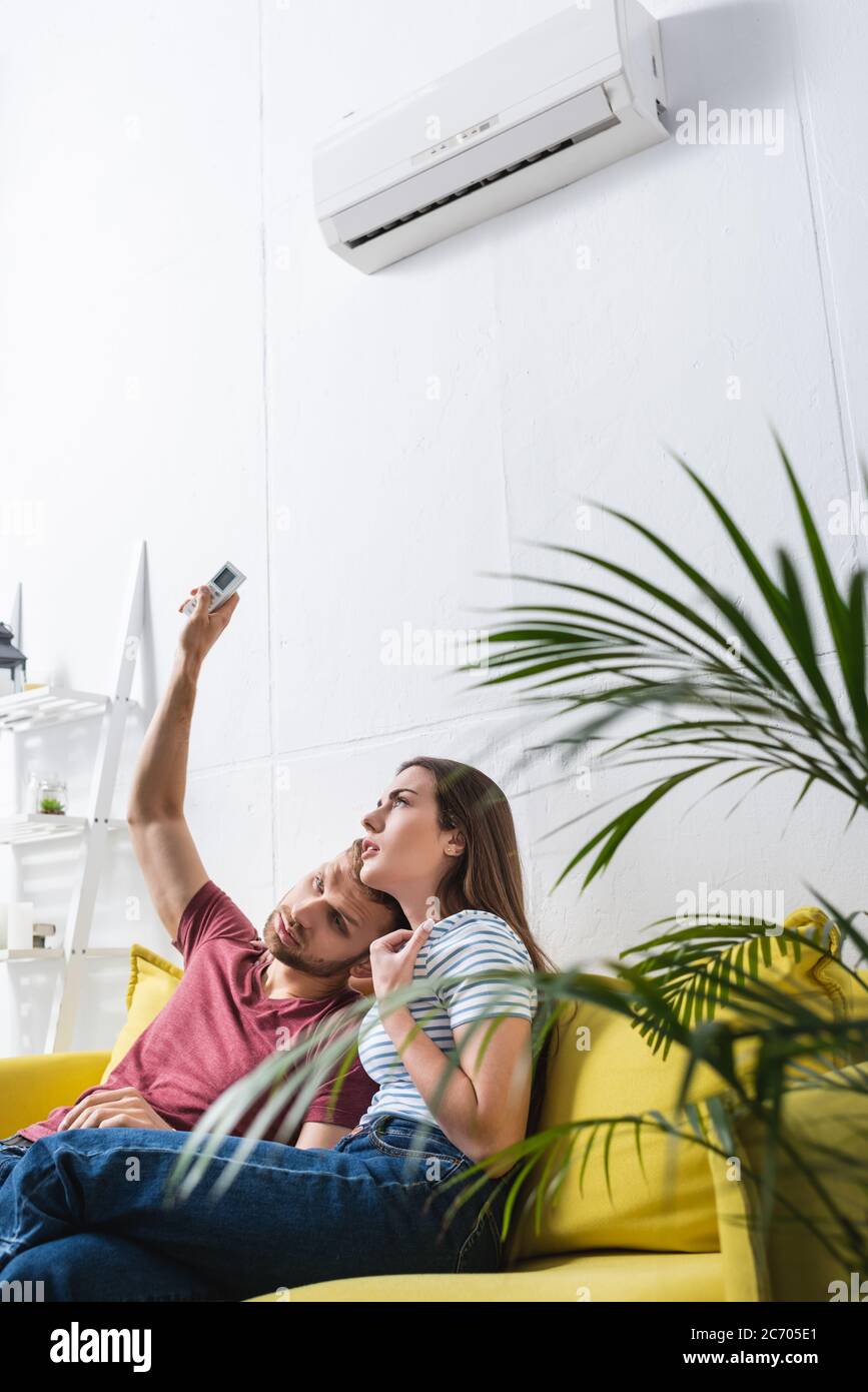 sad couple with remote controller suffering from heat at home with ...