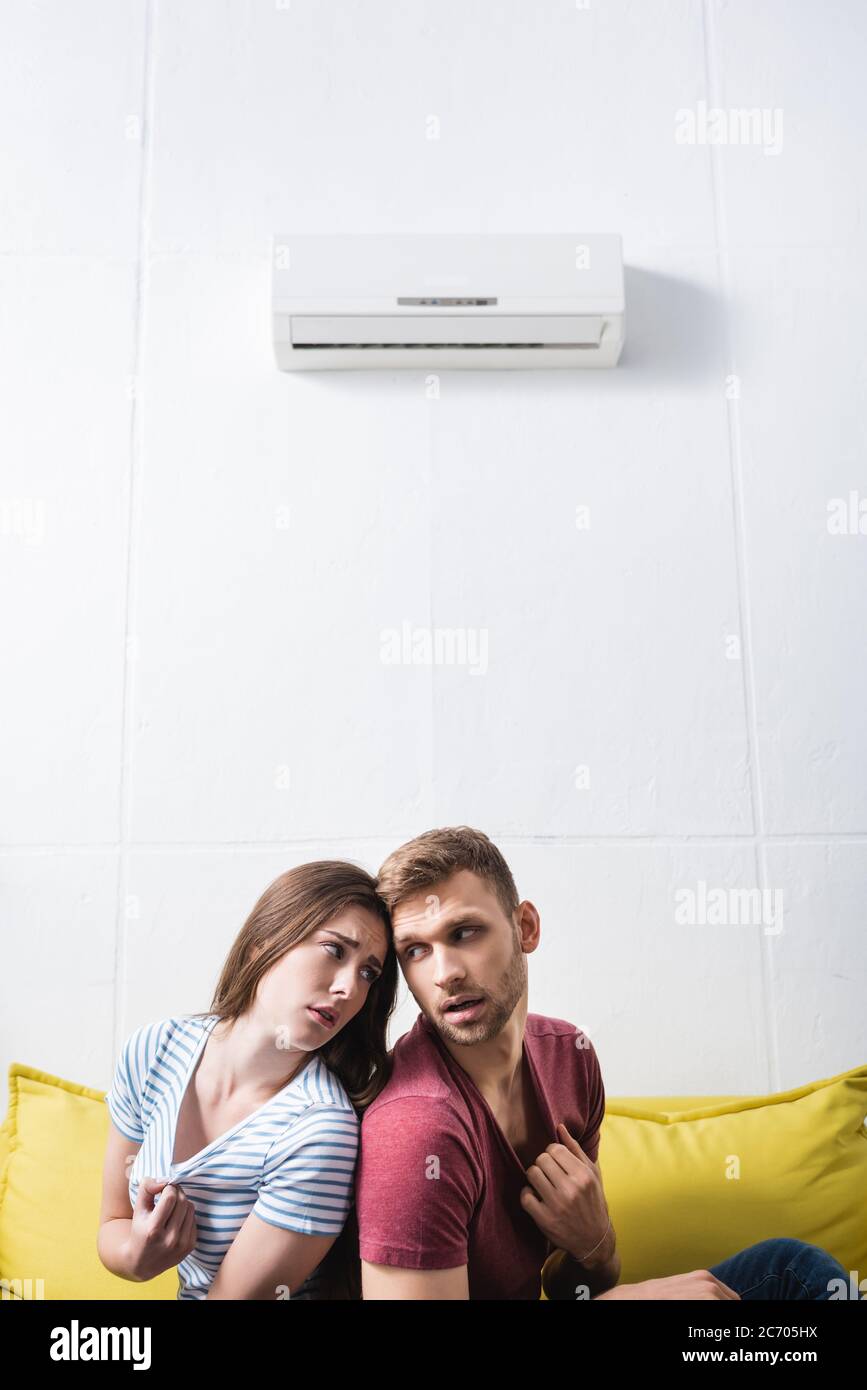sad couple suffering from heat while sitting home with broken air ...