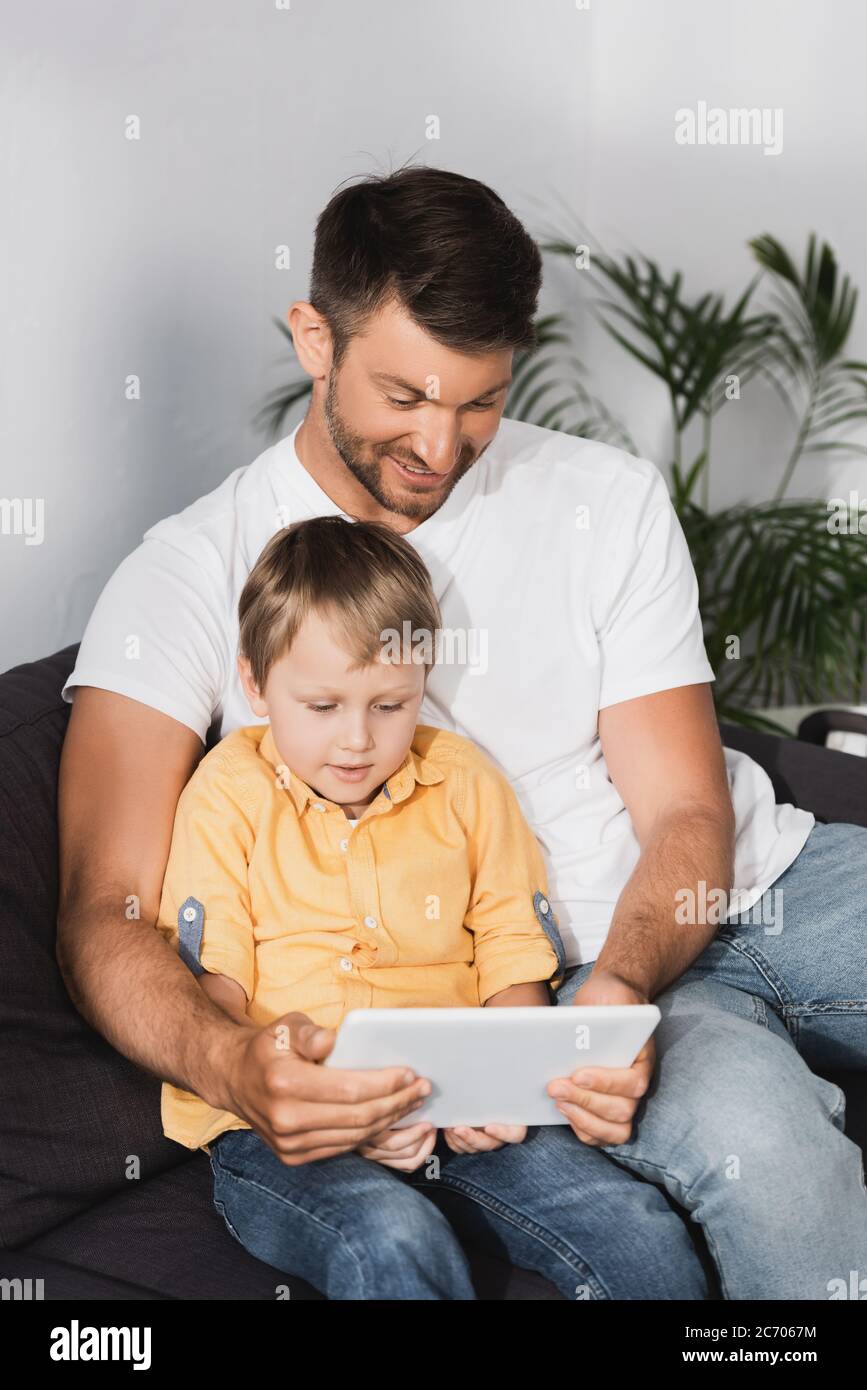 happy father with attentive son sitting on sofa and using laptop ...