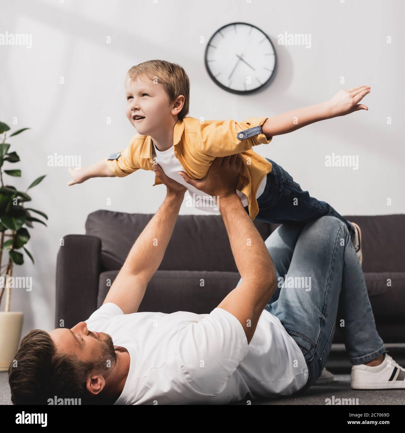 father lying in floor and holding adorabe son imitating flying with ...