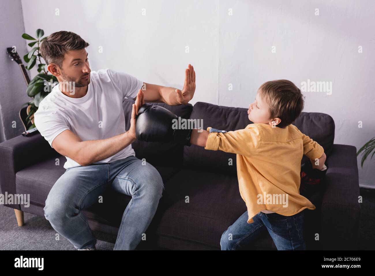 cute boy in boxing gloves fighting with father sitting on sofa Stock ...