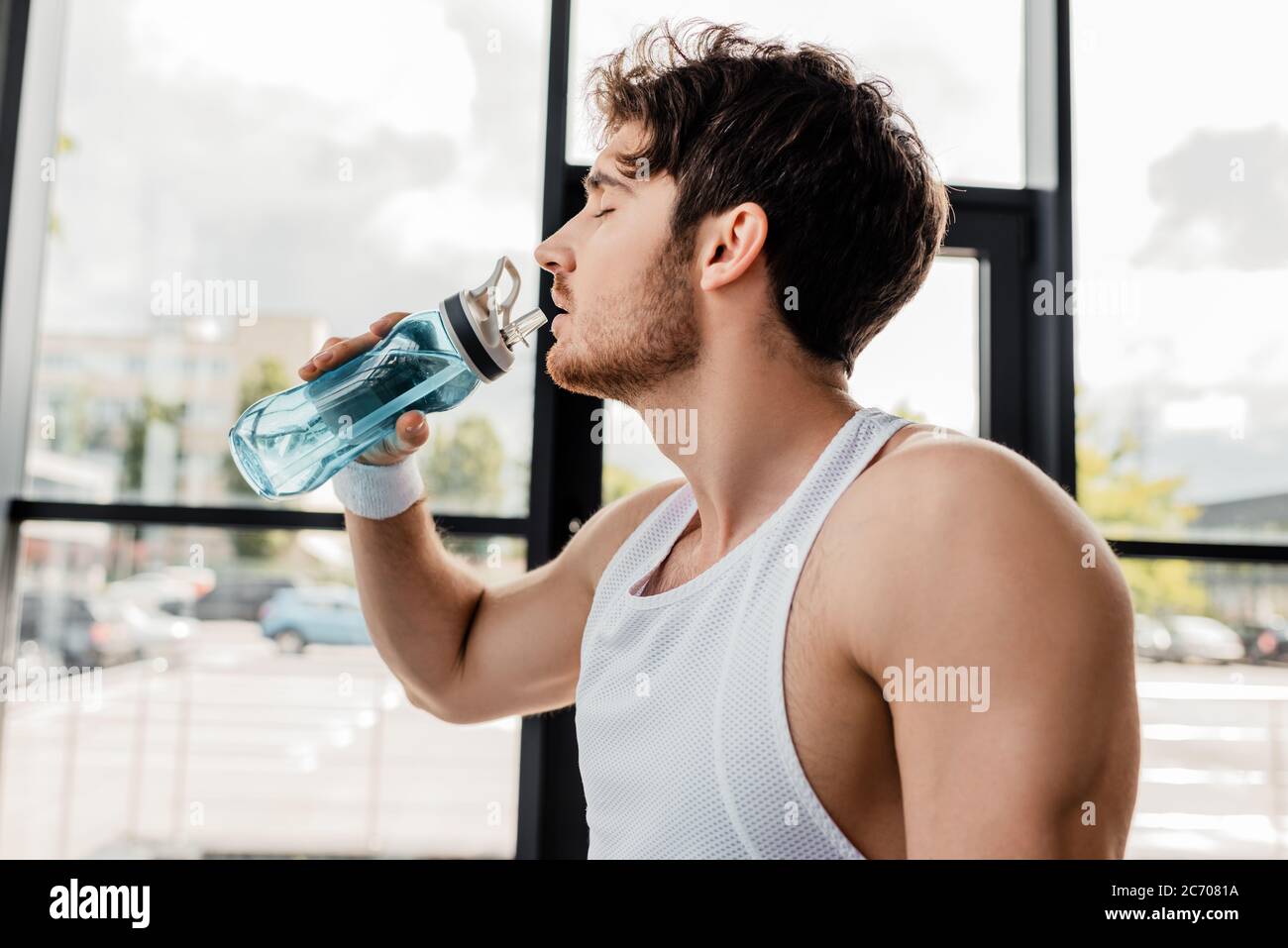 side view of sportsman with closed eyes drinking water and holding ...