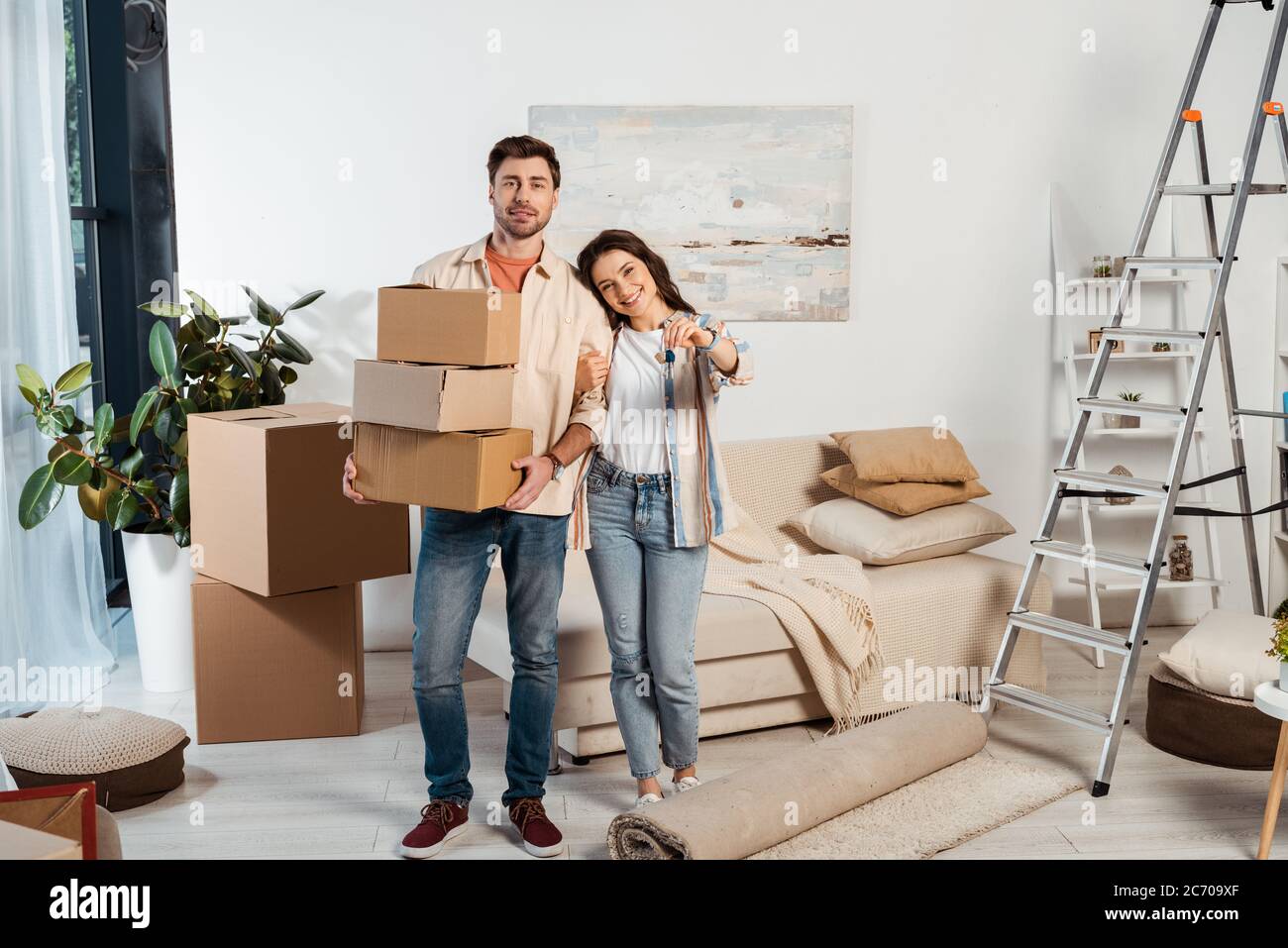 Positive woman holding keys of new house near boyfriend with cardboard ...