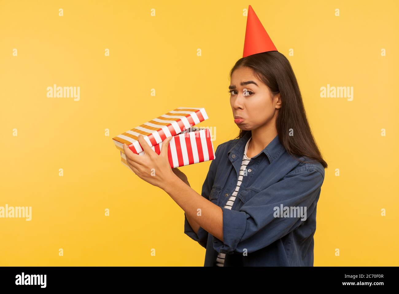 Awful present! Portrait of upset girl in denim shirt and funny cone hat ...