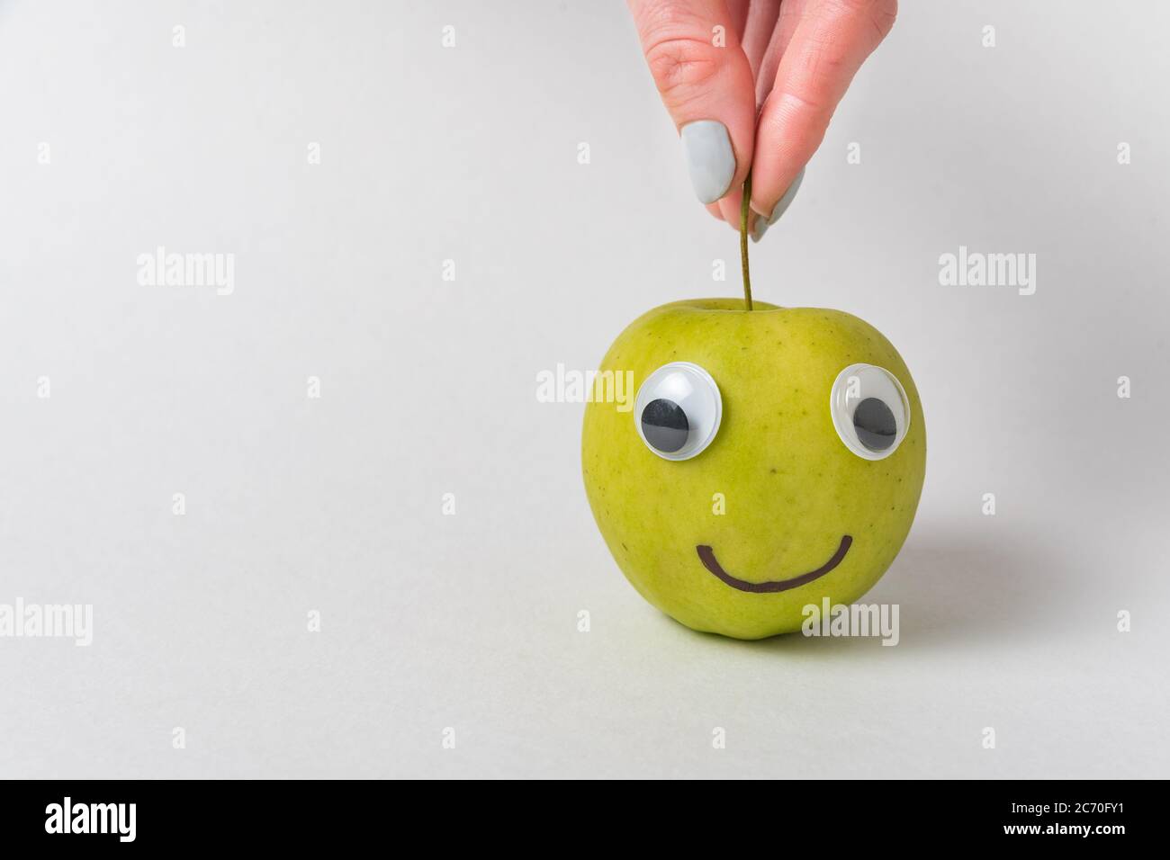 Fingers holding an Apple for the stalk. Apple-smiley with funny face on ...