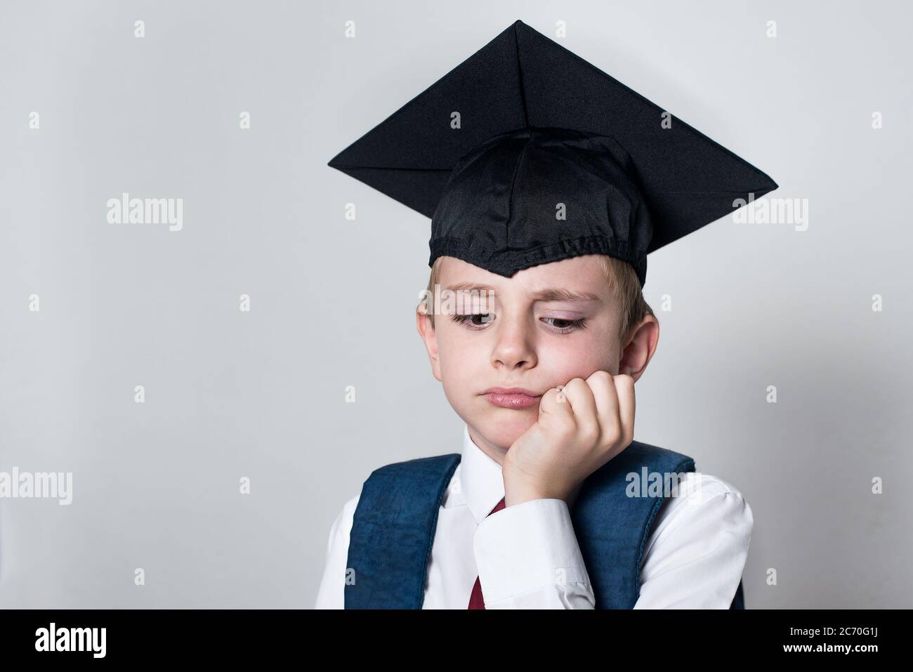 Sad boy in a student hat propped his head with his hand. Failed exam ...