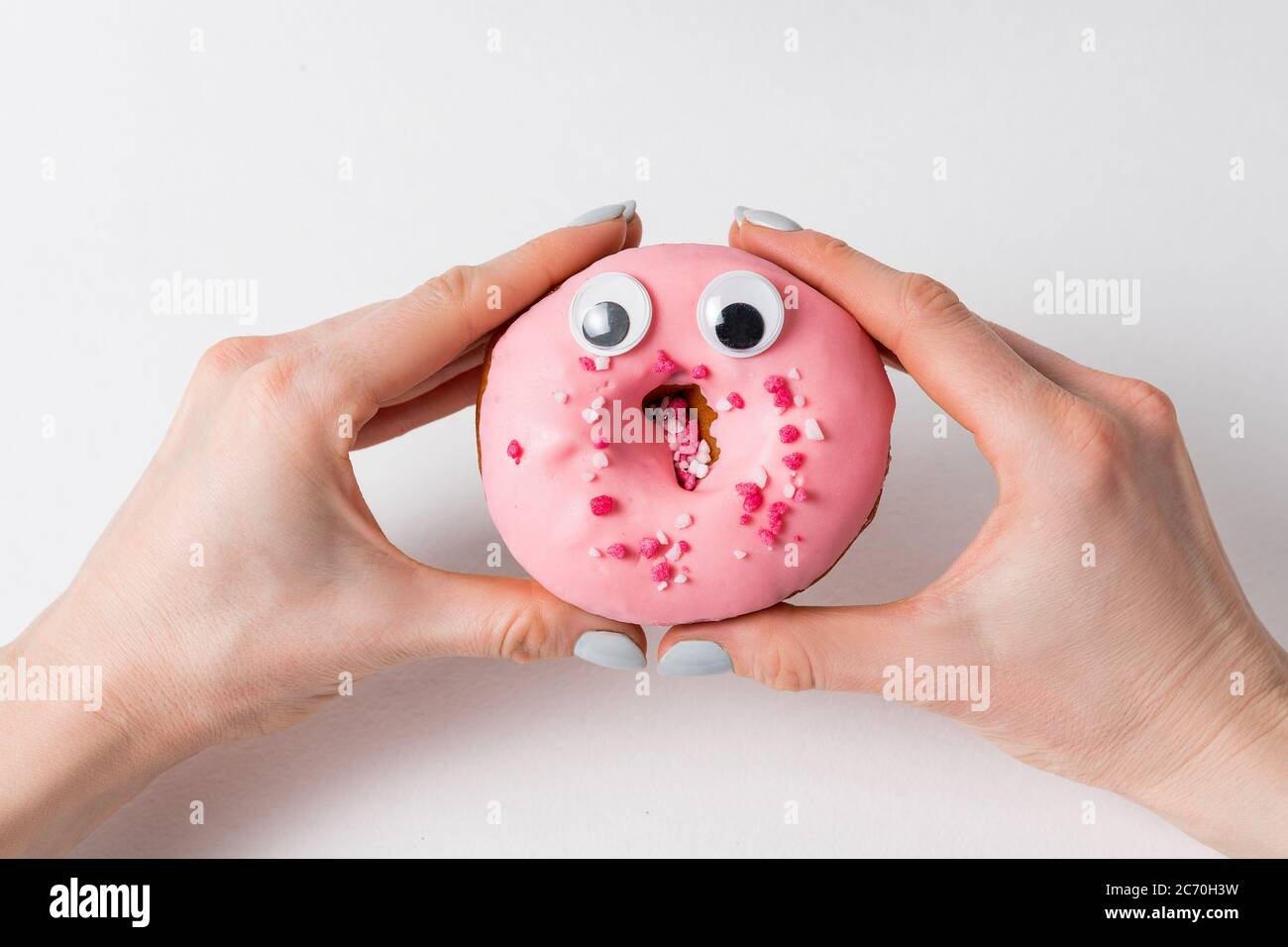 Female hand holding a cute pink donut with a funny face and eyes ...