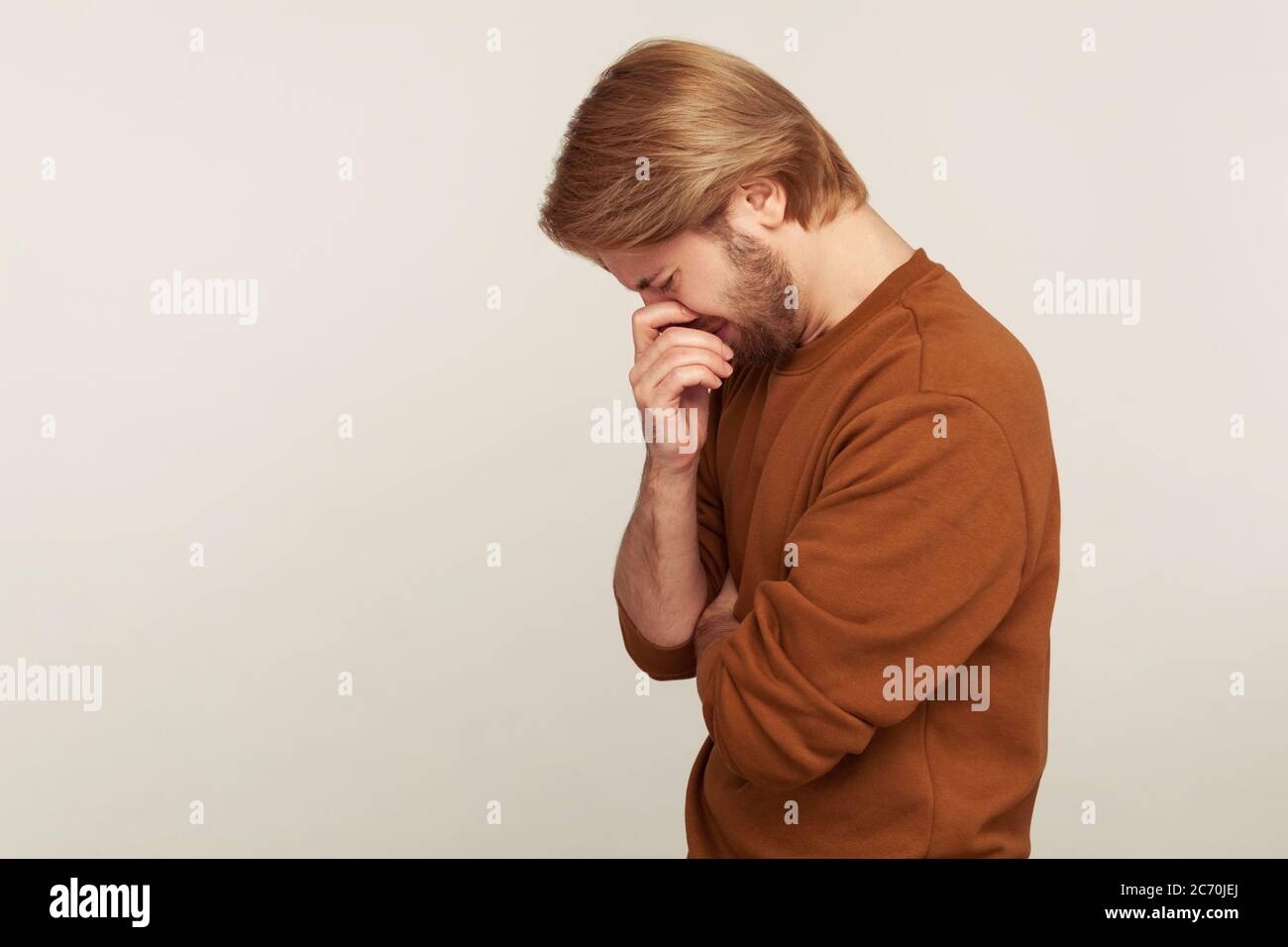 Side view of upset crying man bowing head wiping tears, hiding face and ...