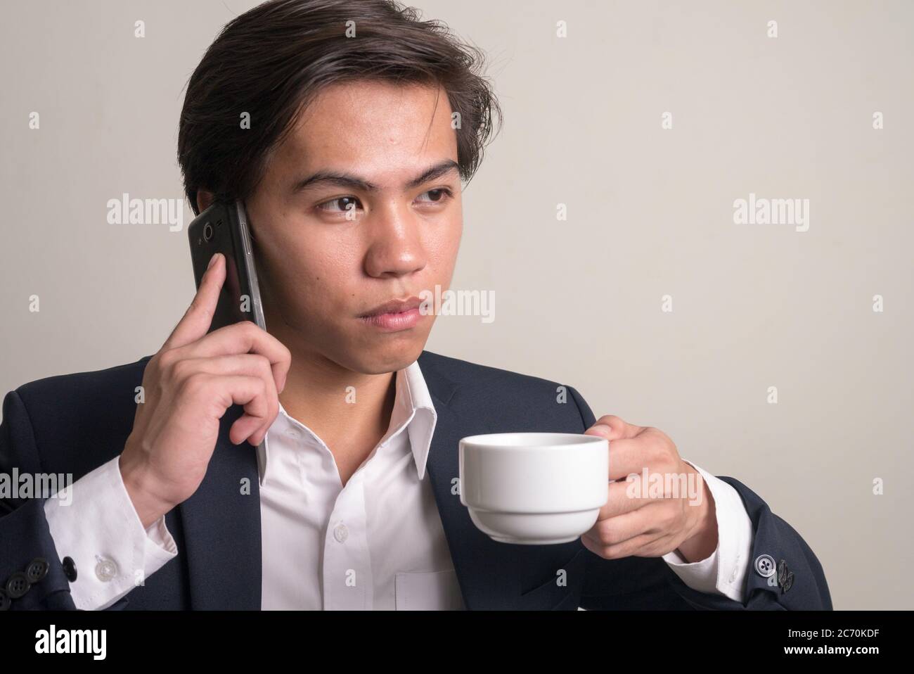 Face of young Filipino businessman in suit talking on the phone and ...