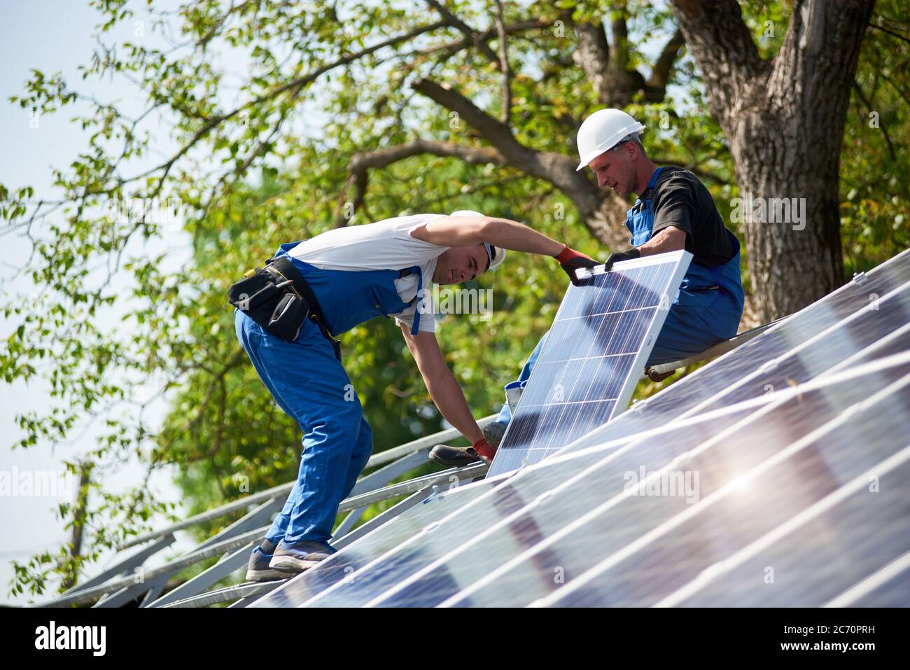 Team of technicians mounting heavy solar photo voltaic panel on tall ...