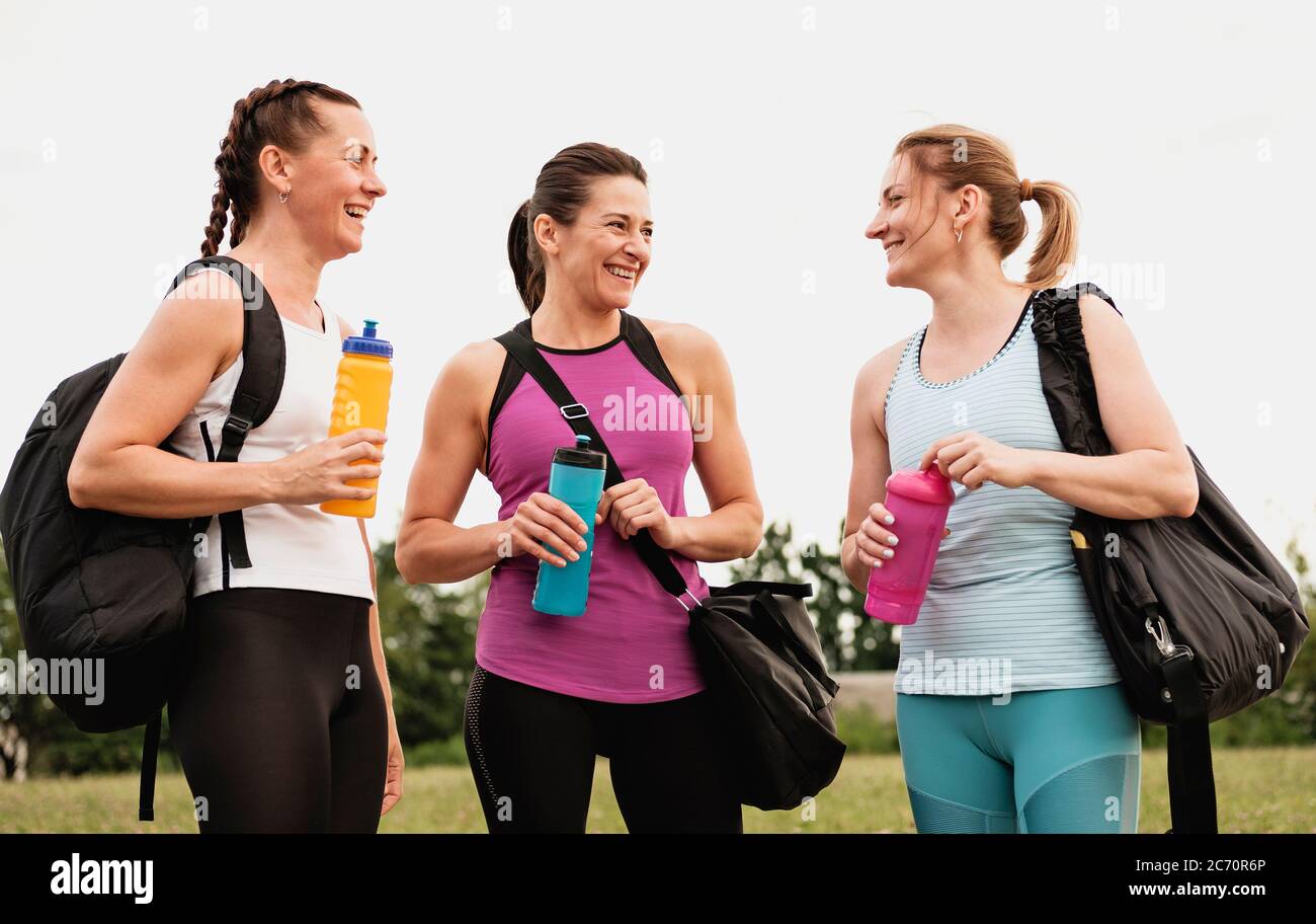 Three healthy fit young women standing chatting together with college ...