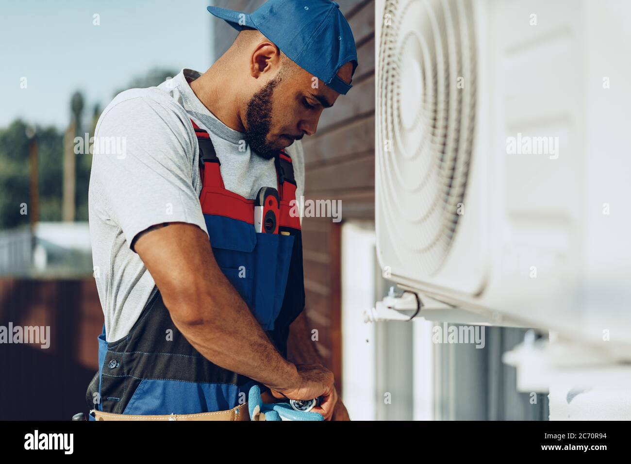 Young black man repairman checking an outside air conditioner unit ...