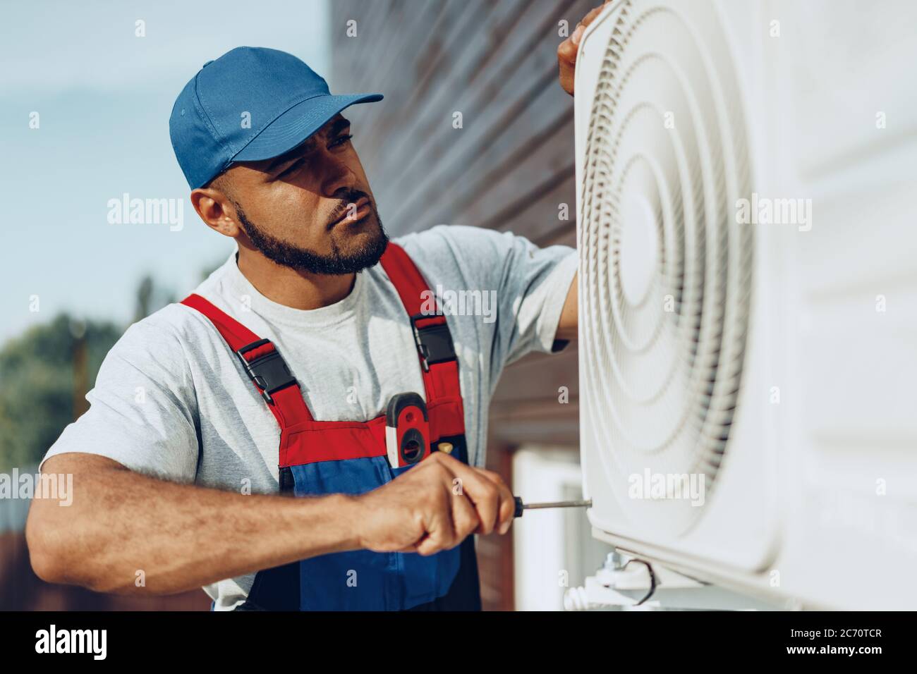 Young black man repairman checking an outside air conditioner unit ...