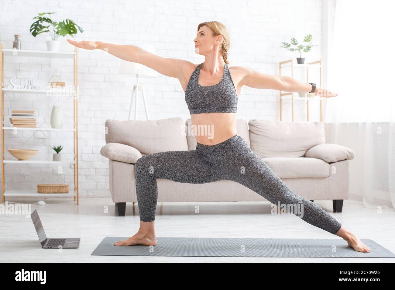 Working with body. Middle aged woman stands at warrior pose on mat with ...