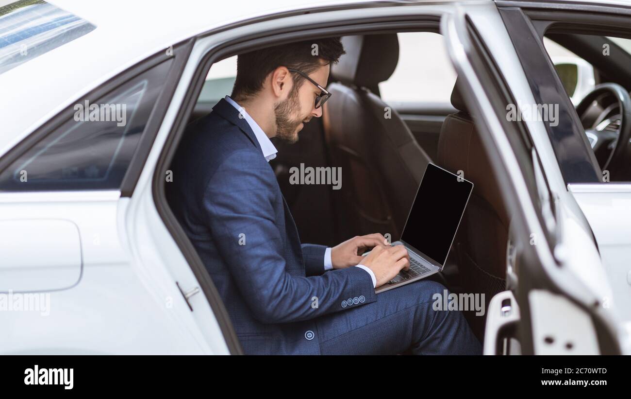 Young businessman using laptop computer with empty screen on back seat ...