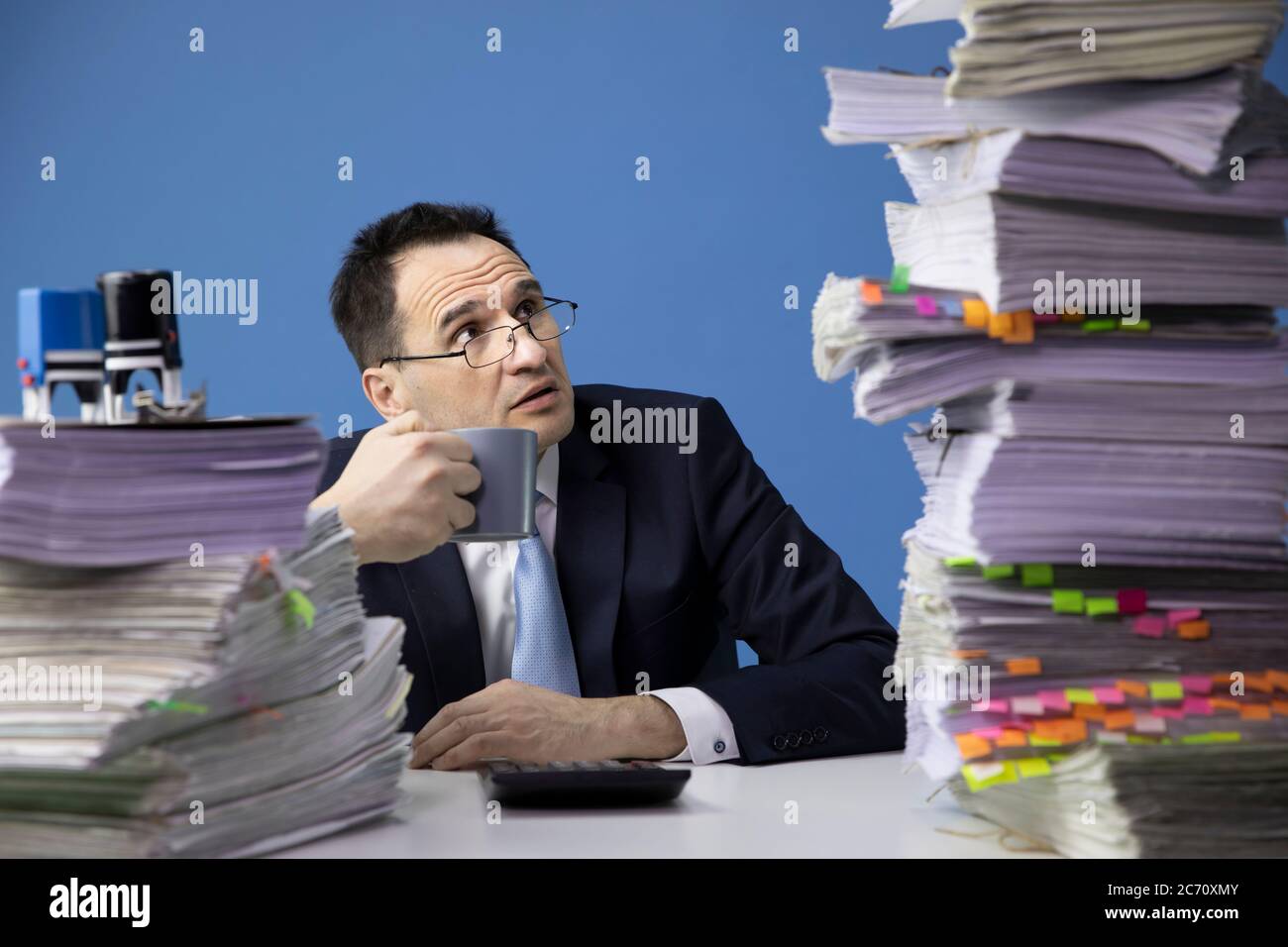 Office worker looks in surprise at huge stack papers on desktop in ...