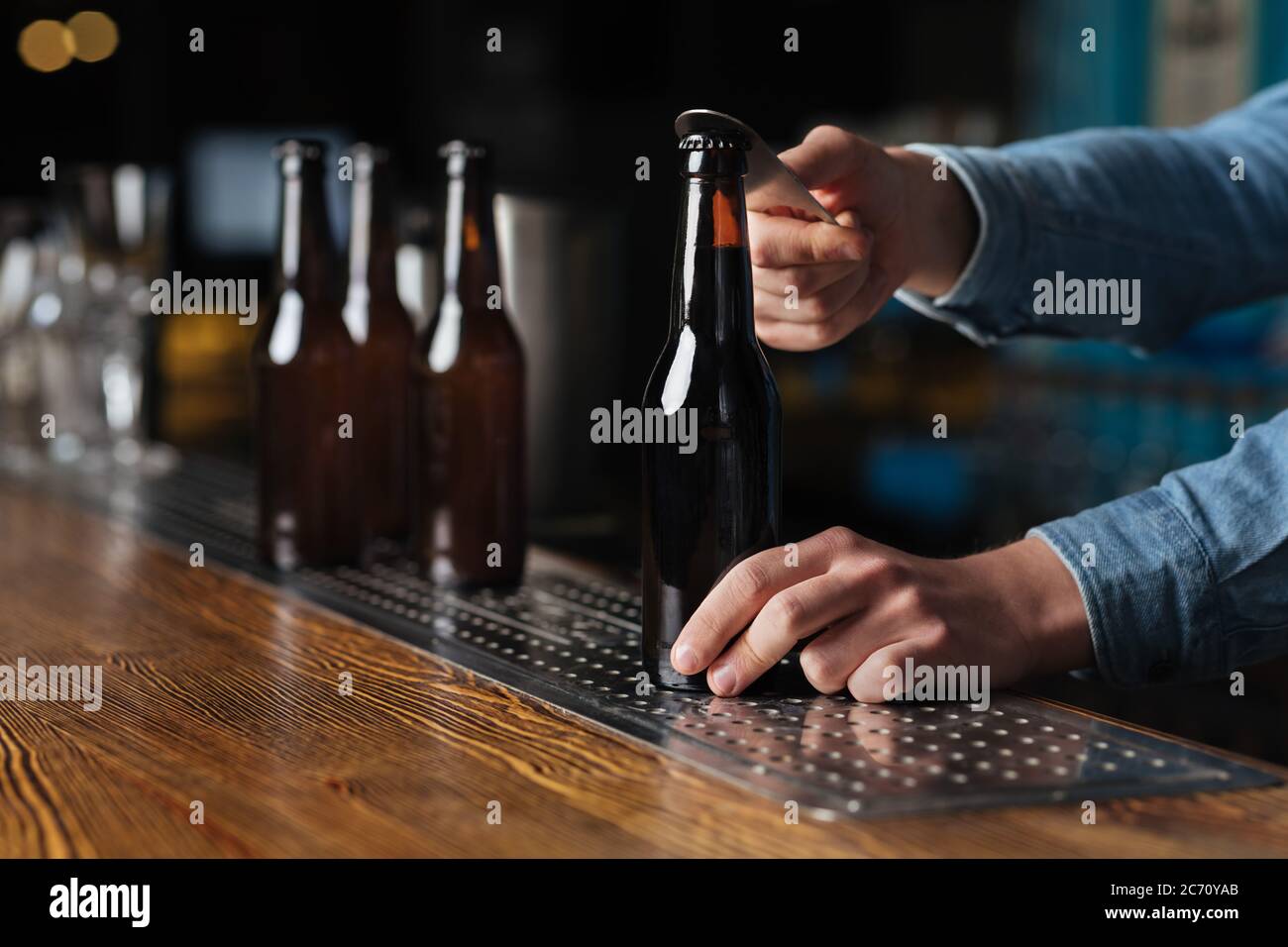 Bartender hands open bottle of beer in a dark bar interior Stock Photo ...