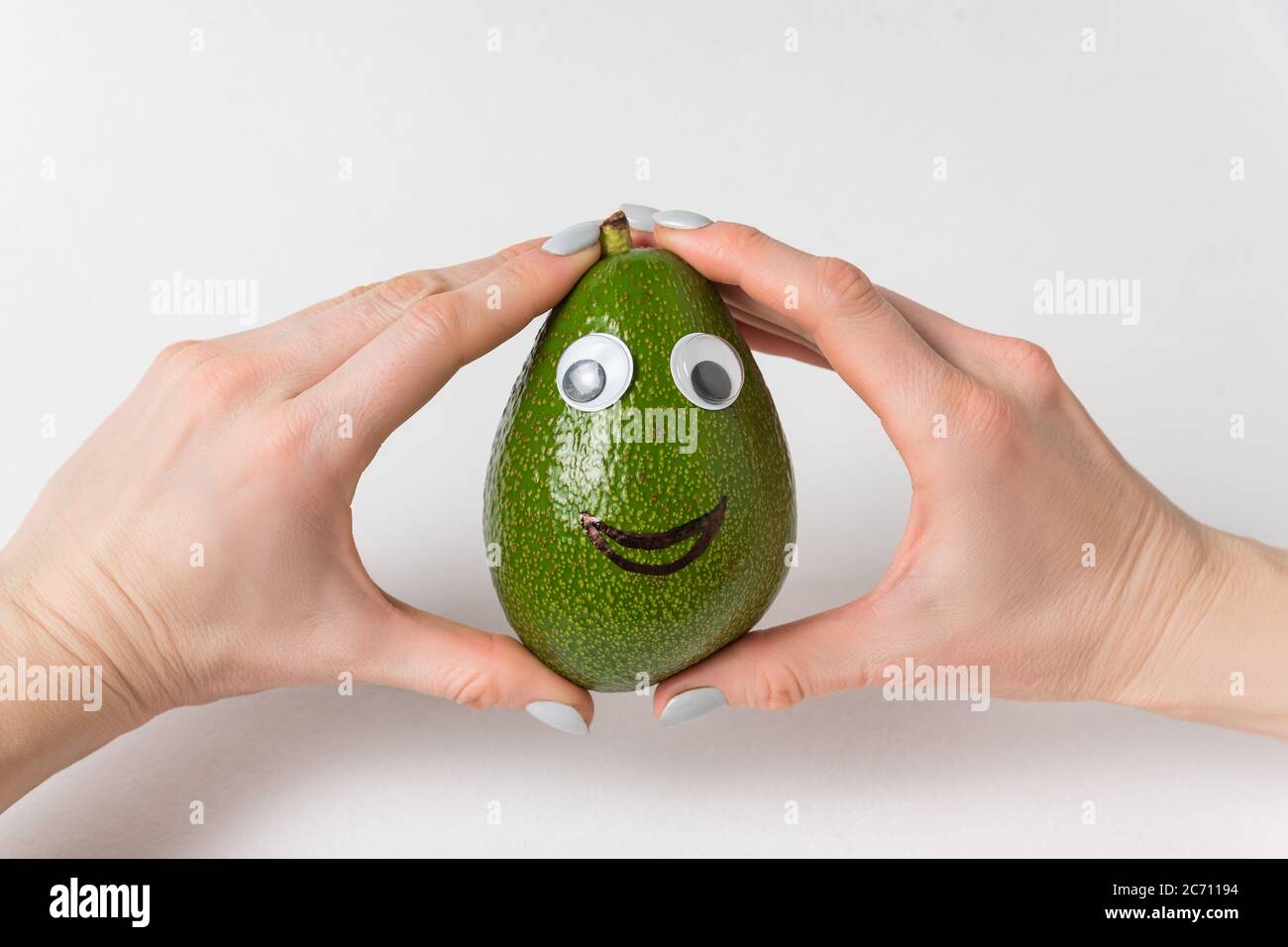 female hands holds avocado with funny face. Avocado with Googly eyes ...