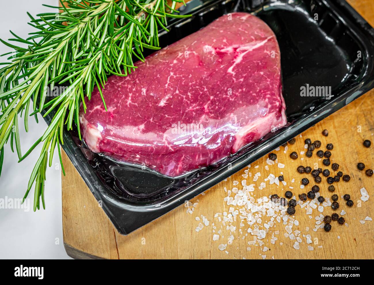 Beef steak in vacuum skin packaging and spices on wooden chopping board ...