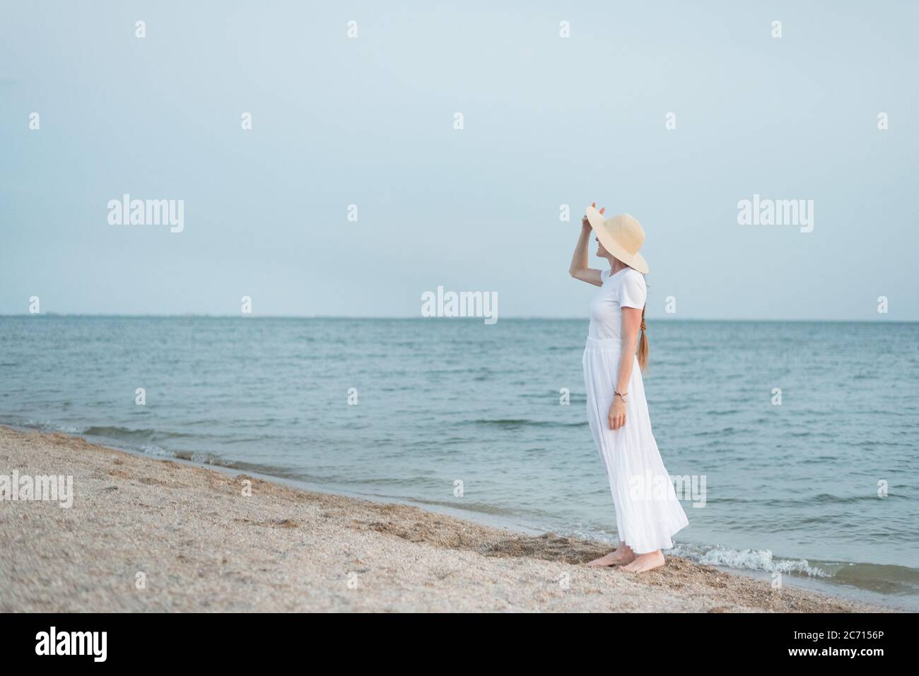 Young fragile woman in long white dress standing at edge of water on ...