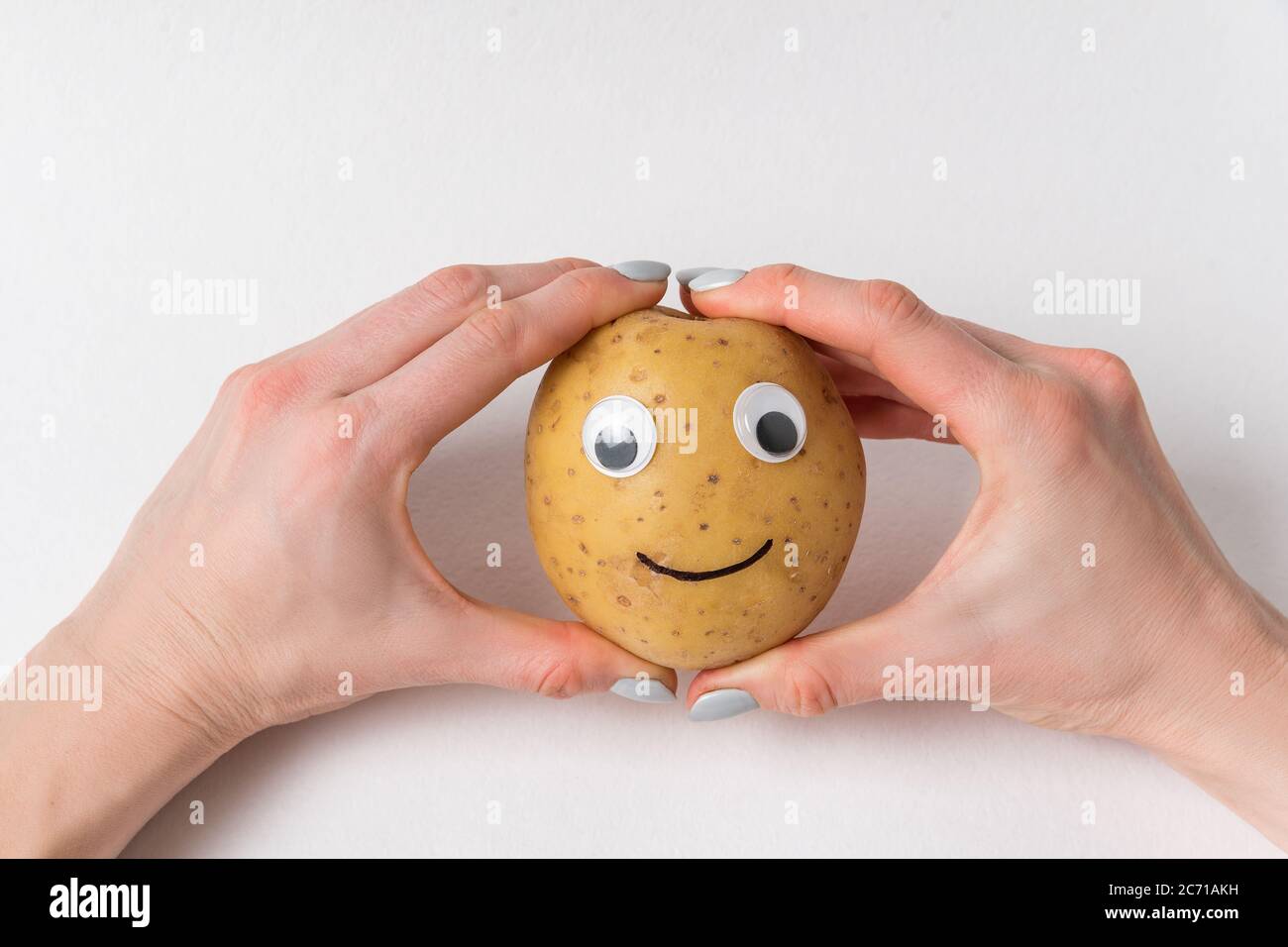 Hands holding raw potatoes with Googly eyes and smile. Vegetables with ...